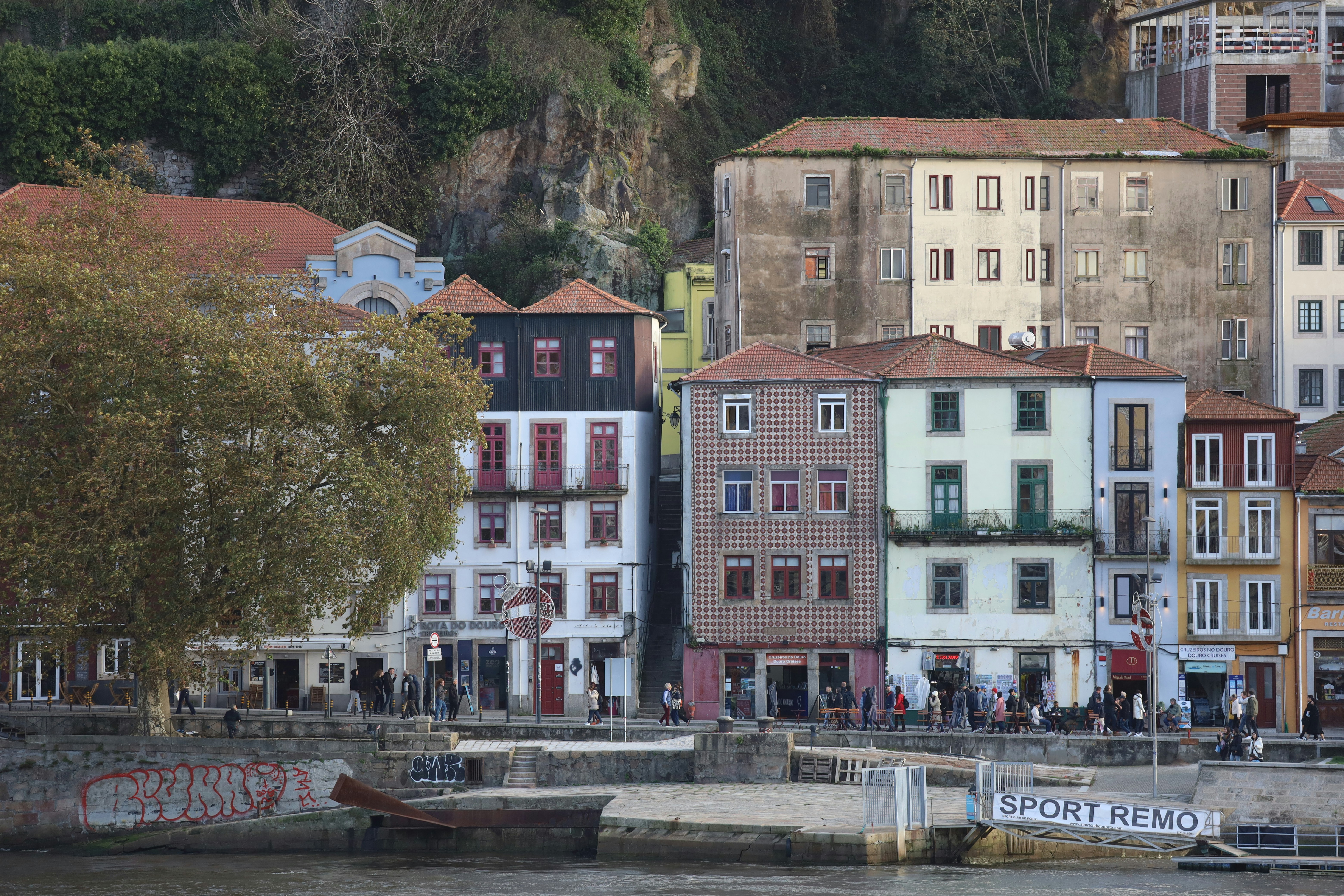 Colorful waterfront buildings with a backdrop of lush greenery and autumn foliage.
