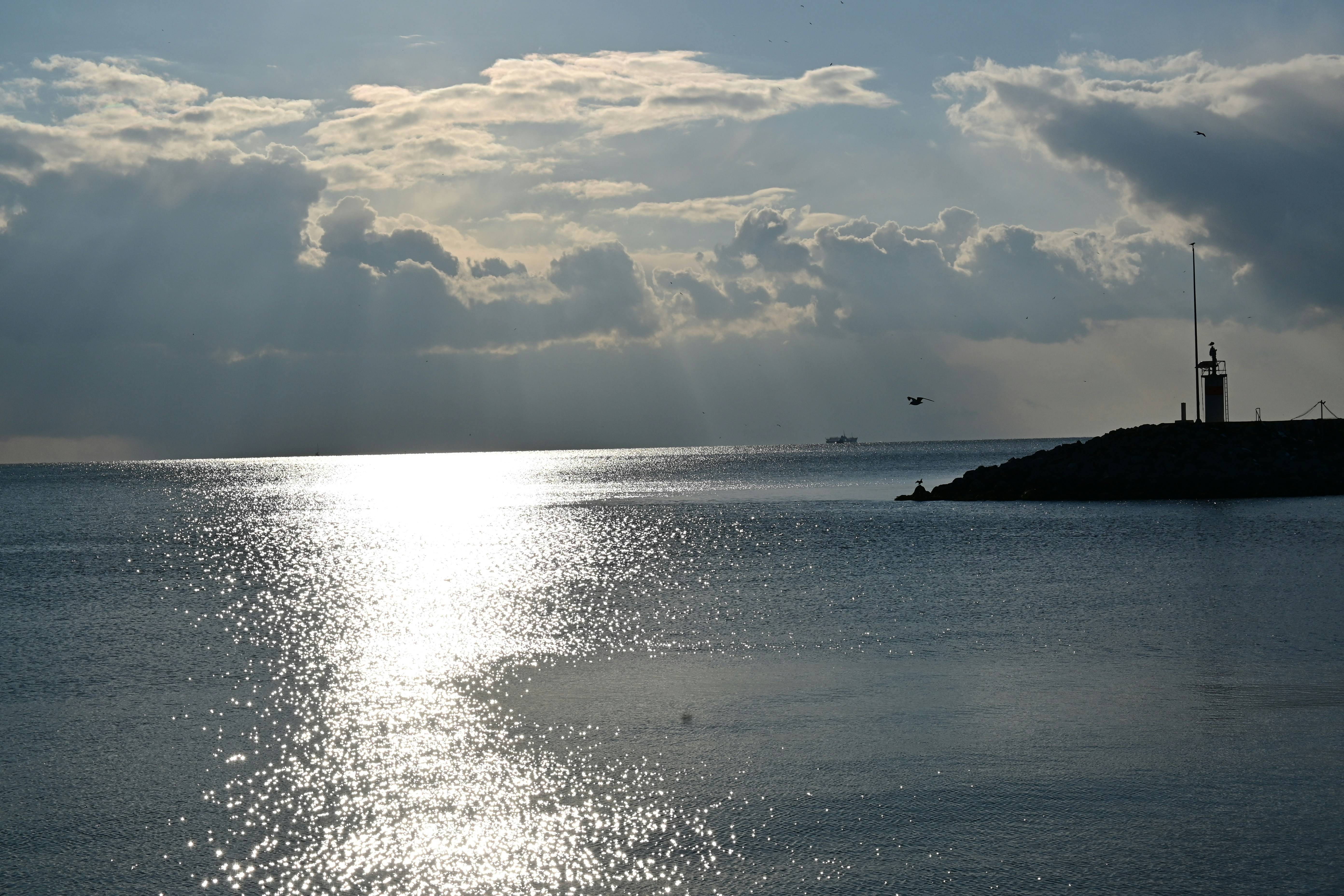 Sunlight reflecting off the sea with a silhouette of a lighthouse and distant clouds.