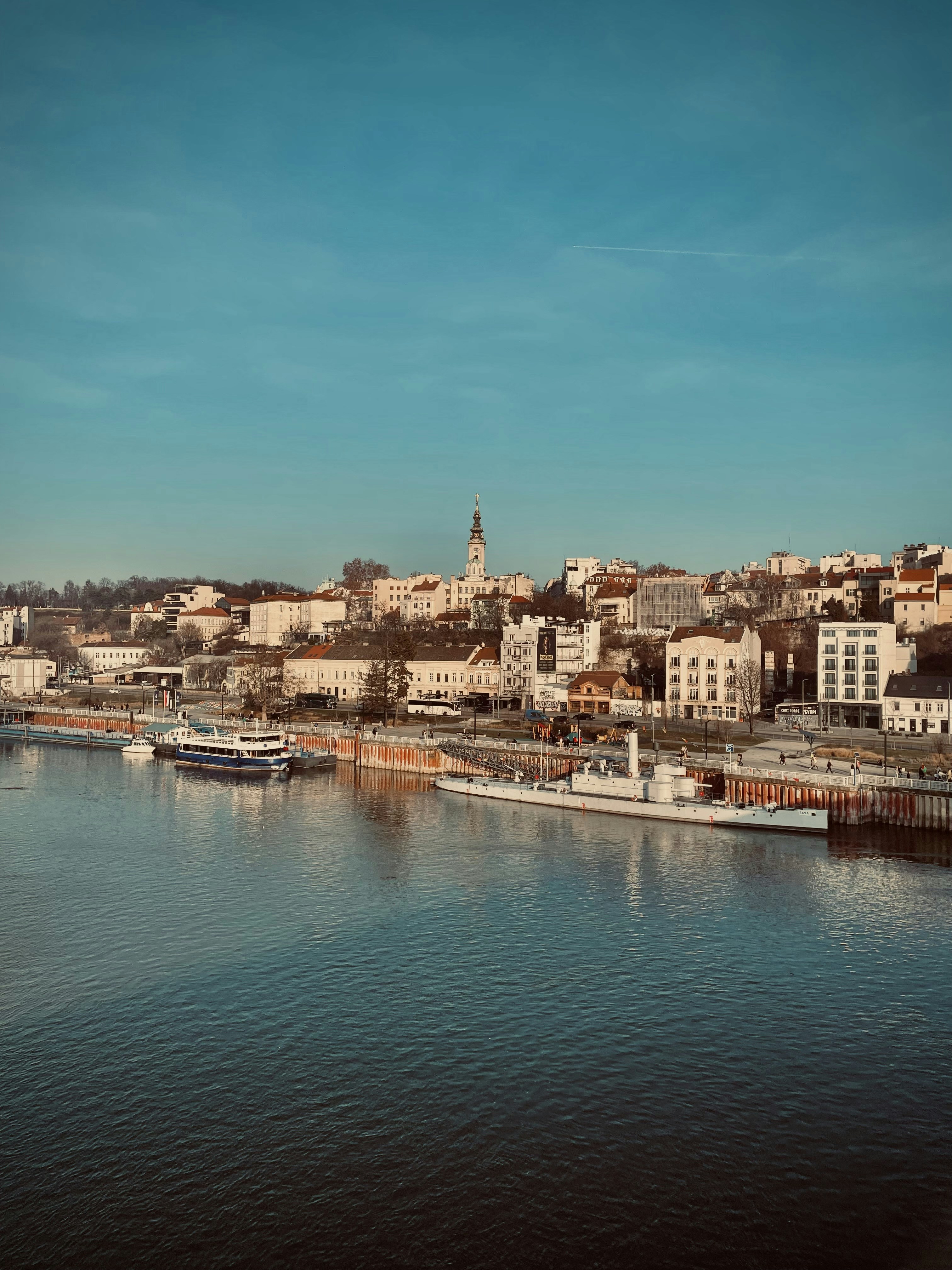 Charming riverside scene featuring boats docked along the waterfront with a backdrop of colorful buildings and a prominent clock tower. 