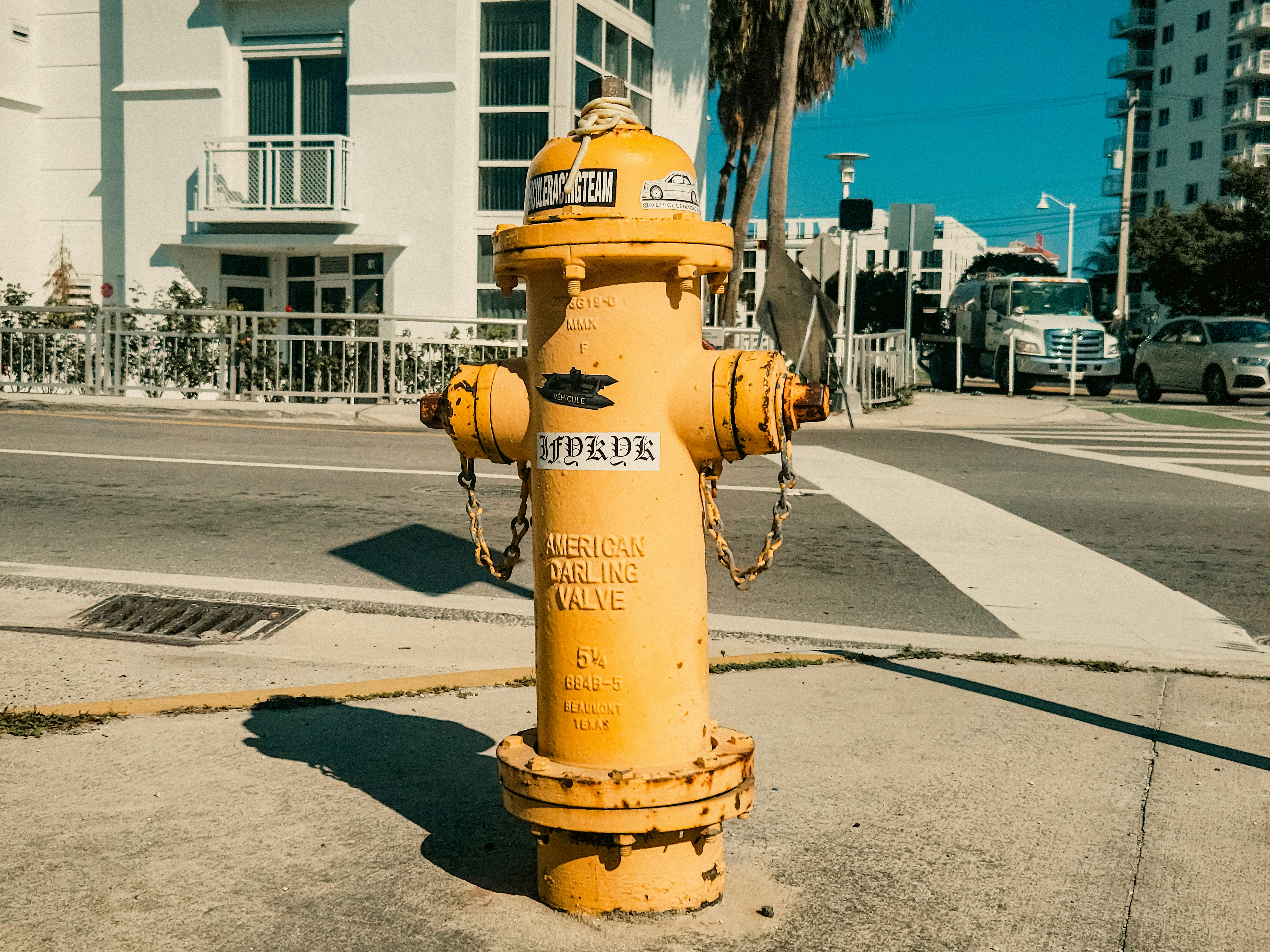 Yellow fire hydrant on a city sidewalk under clear blue sky.