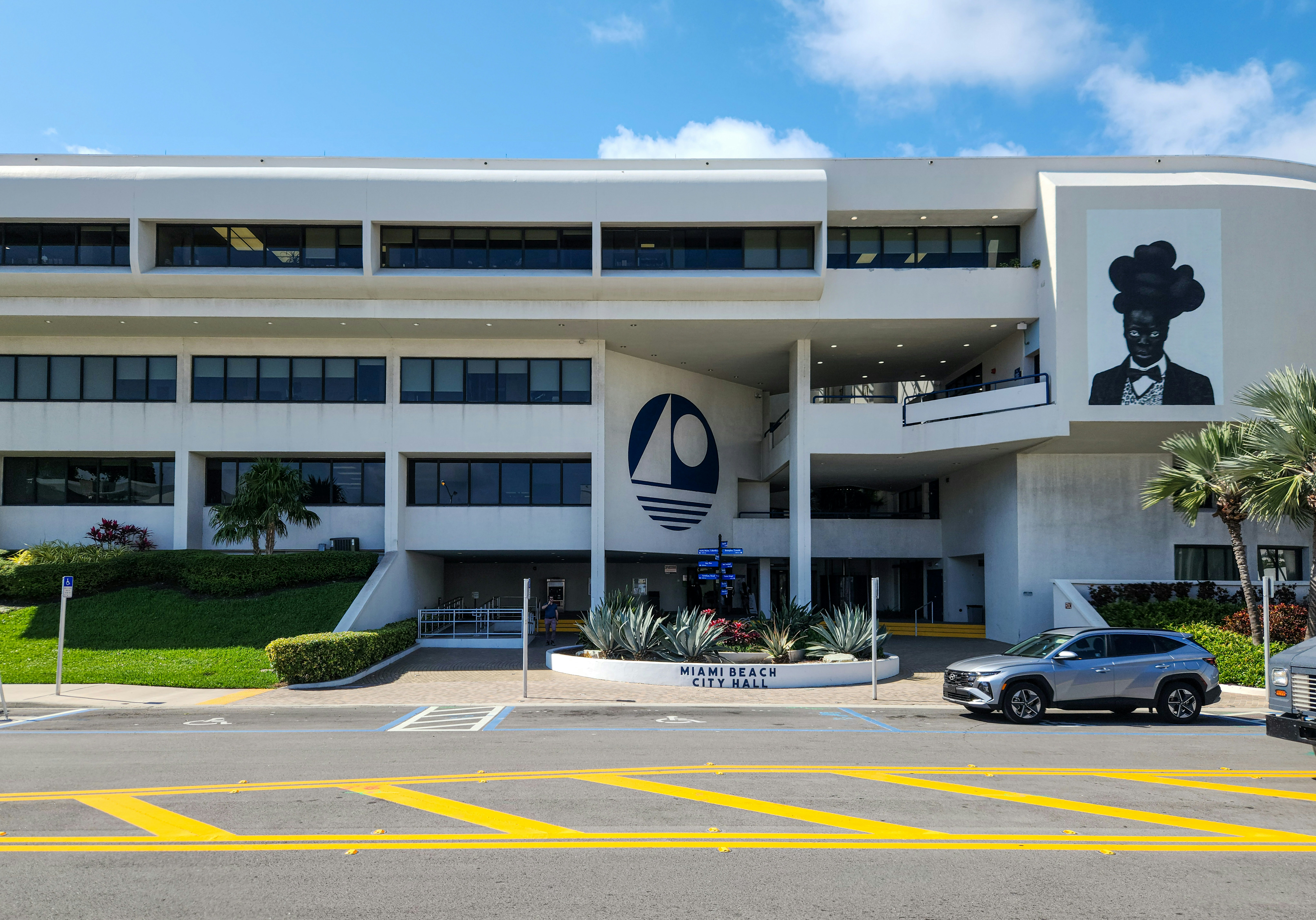 Miami Beach City Hall showcases modernist architecture with a large mural and lush landscaping under a clear blue sky.