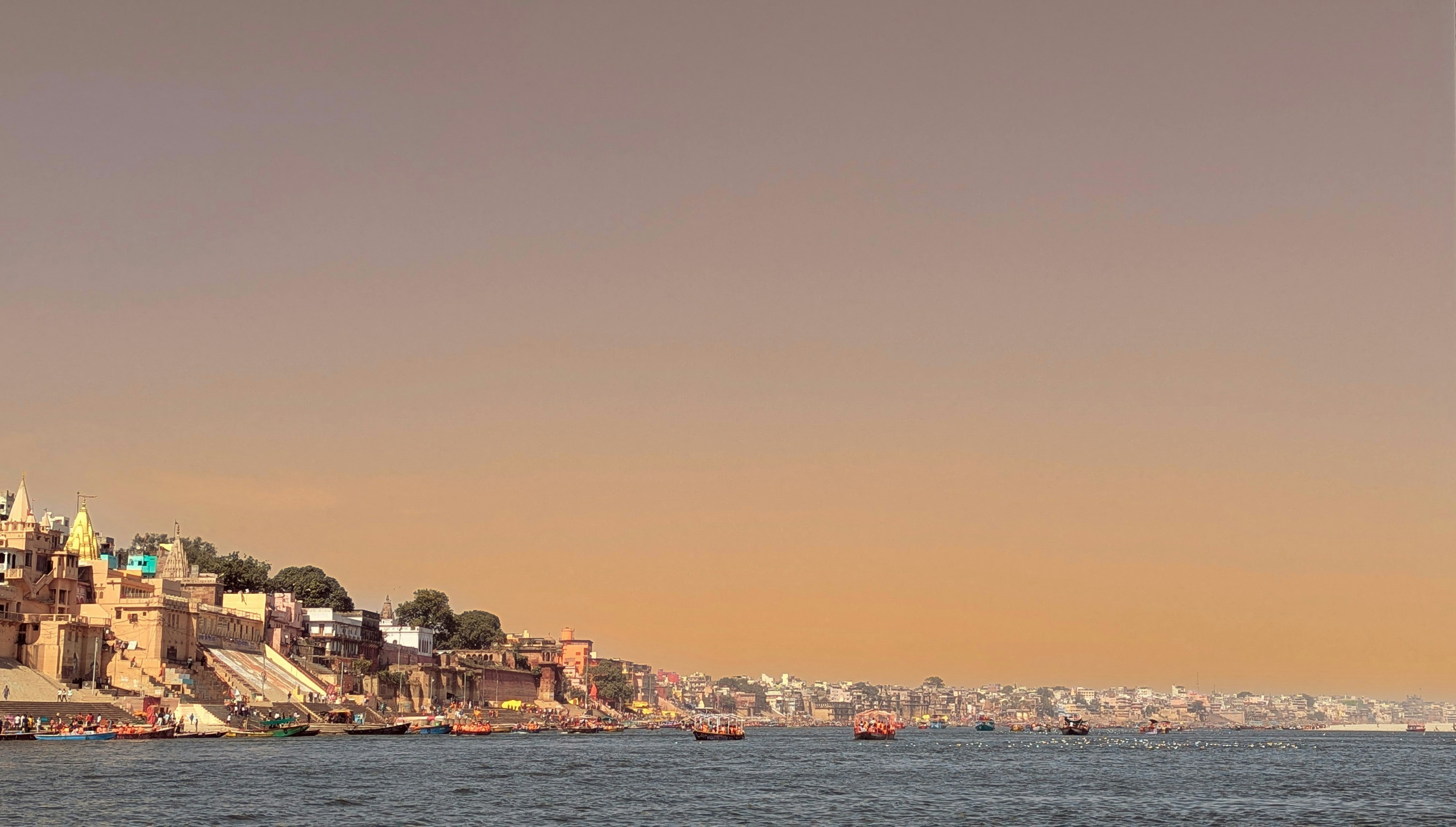 Ancient ghats along the Ganges River under a warm, golden sky.
