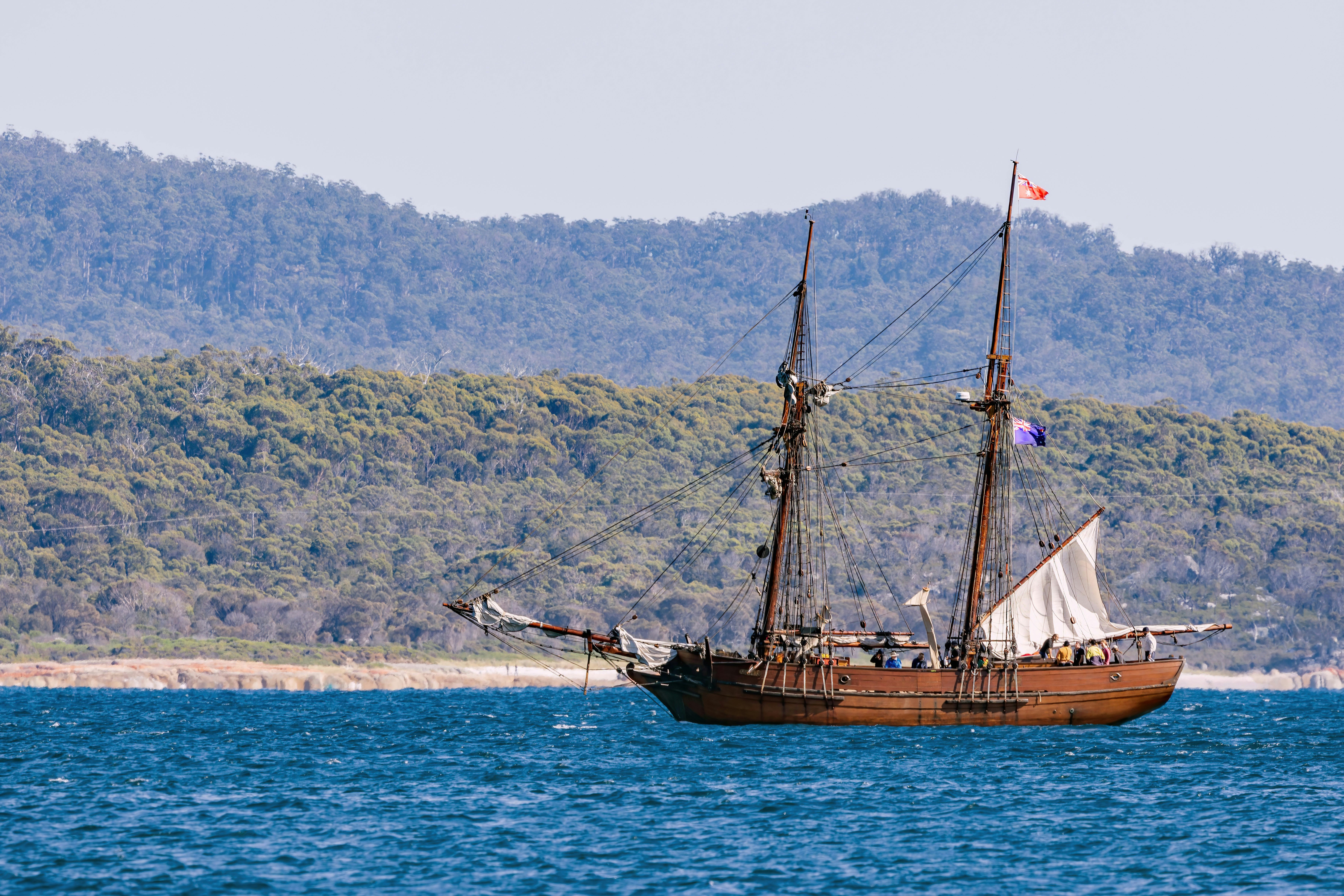 A classic wooden ship gracefully sails through calm waters, framed by lush green hills in the background.
