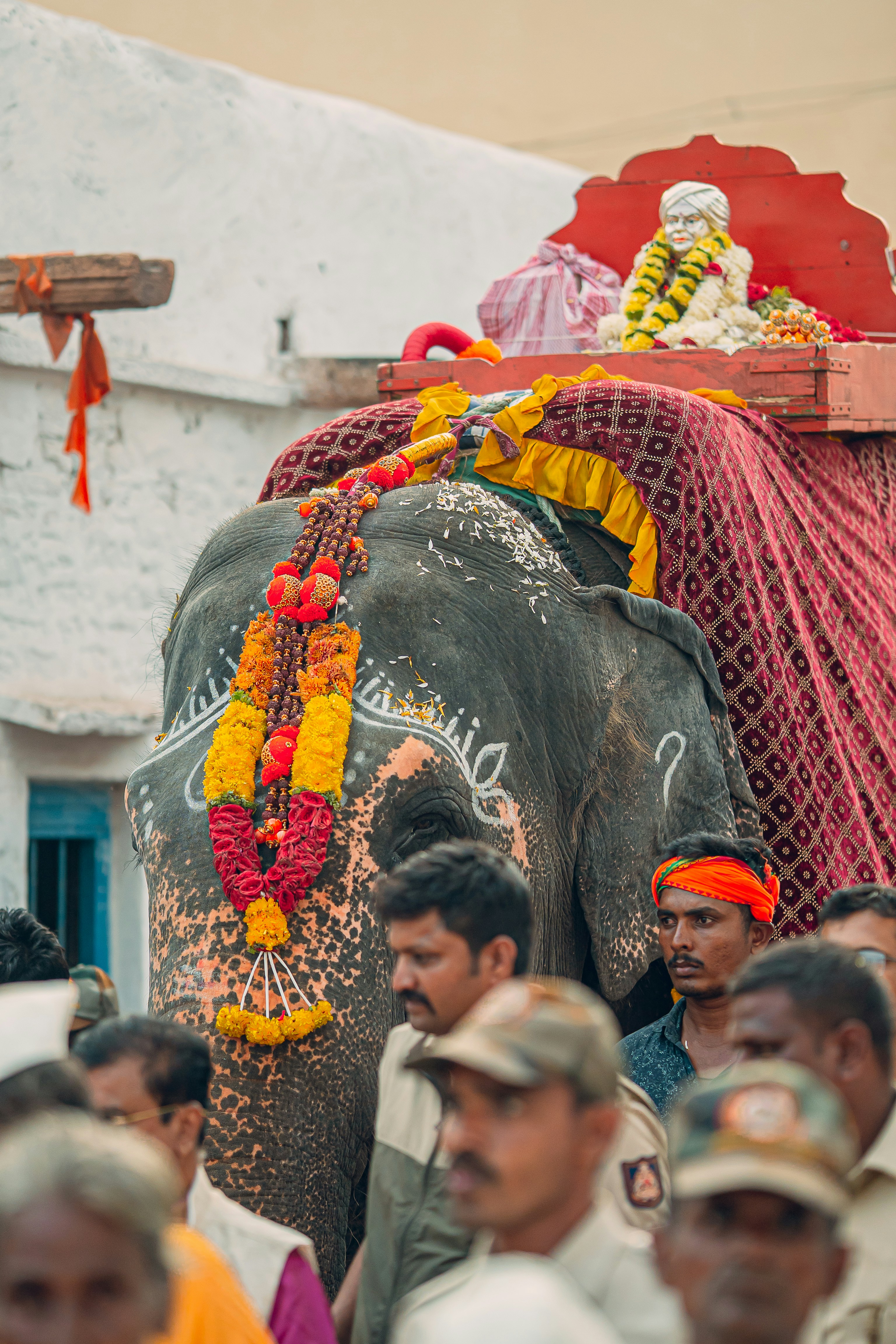 An adorned elephant carries a statue amidst a vibrant crowd during a cultural celebration. The rich colors and intricate details highlight the festive spirit.