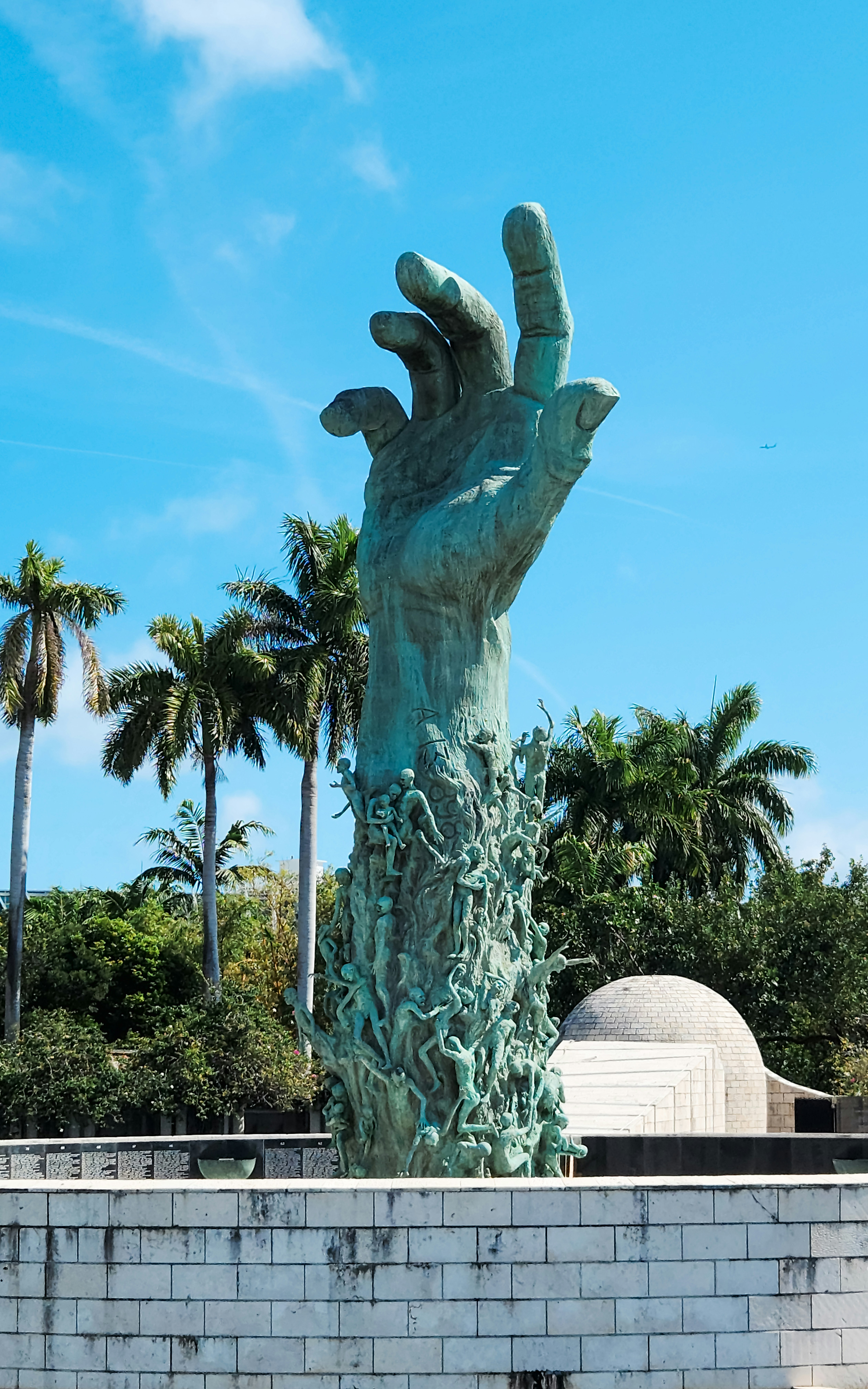 The Holocaust Memorial in Miami Beach, dedicated in 1990, honors the six million Jewish victims of the Holocaust. Designed by architect Kenneth Treister, its centerpiece is a striking 42-foot bronze sculpture of an outstretched hand, surrounded by anguished human figures. The memorial includes a black granite wall inscribed with victims' names, a reflective pool, and an indoor exhibit with historical narratives. Located in a tranquil garden setting, it serves as a place for education, remembrance, and reflection, drawing visitors from around the world.