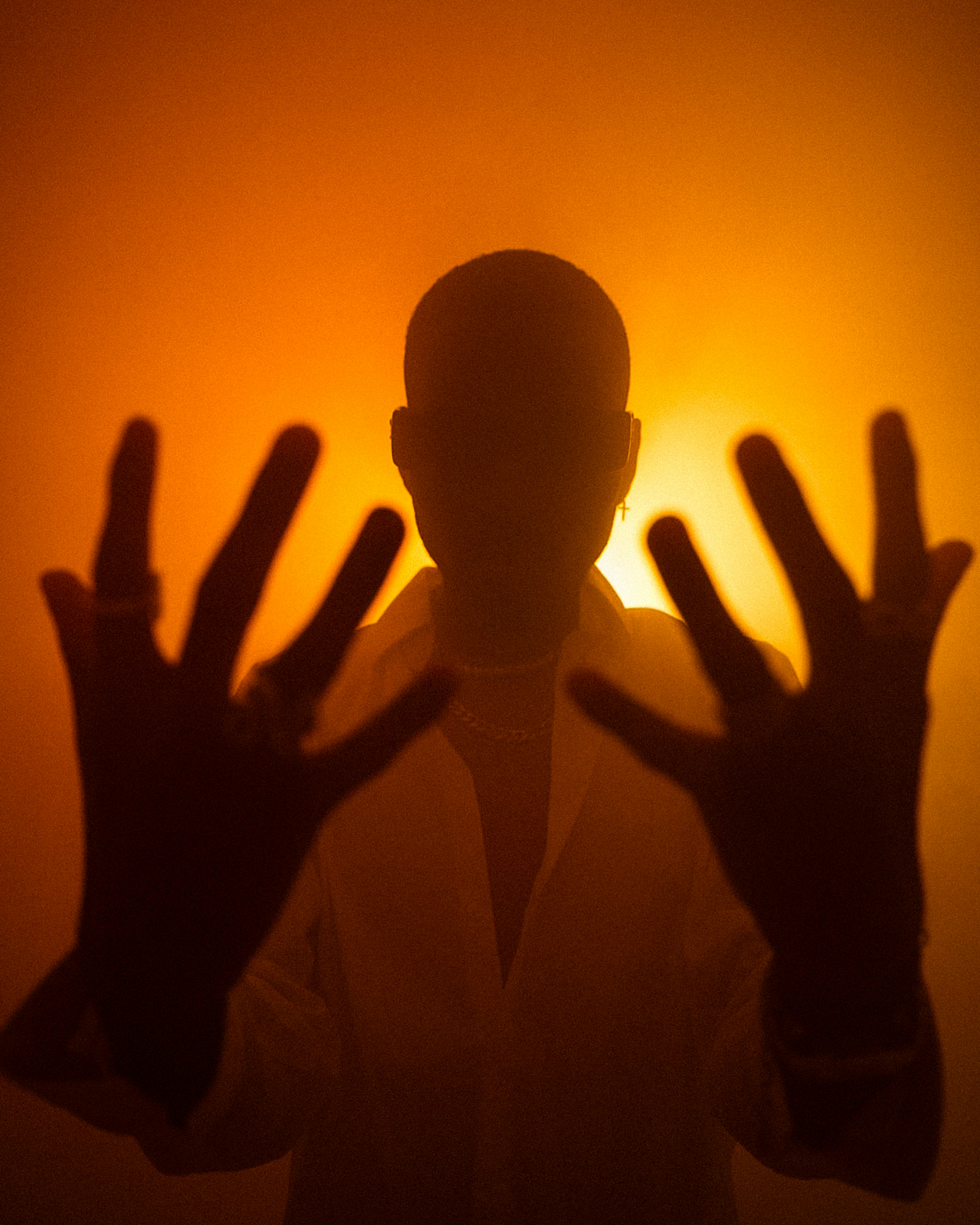 Silhouette of a figure surrounded by an ethereal orange glow, hands outstretched as if breaking through a fog. The scene evokes a sense of intrigue and emotion.