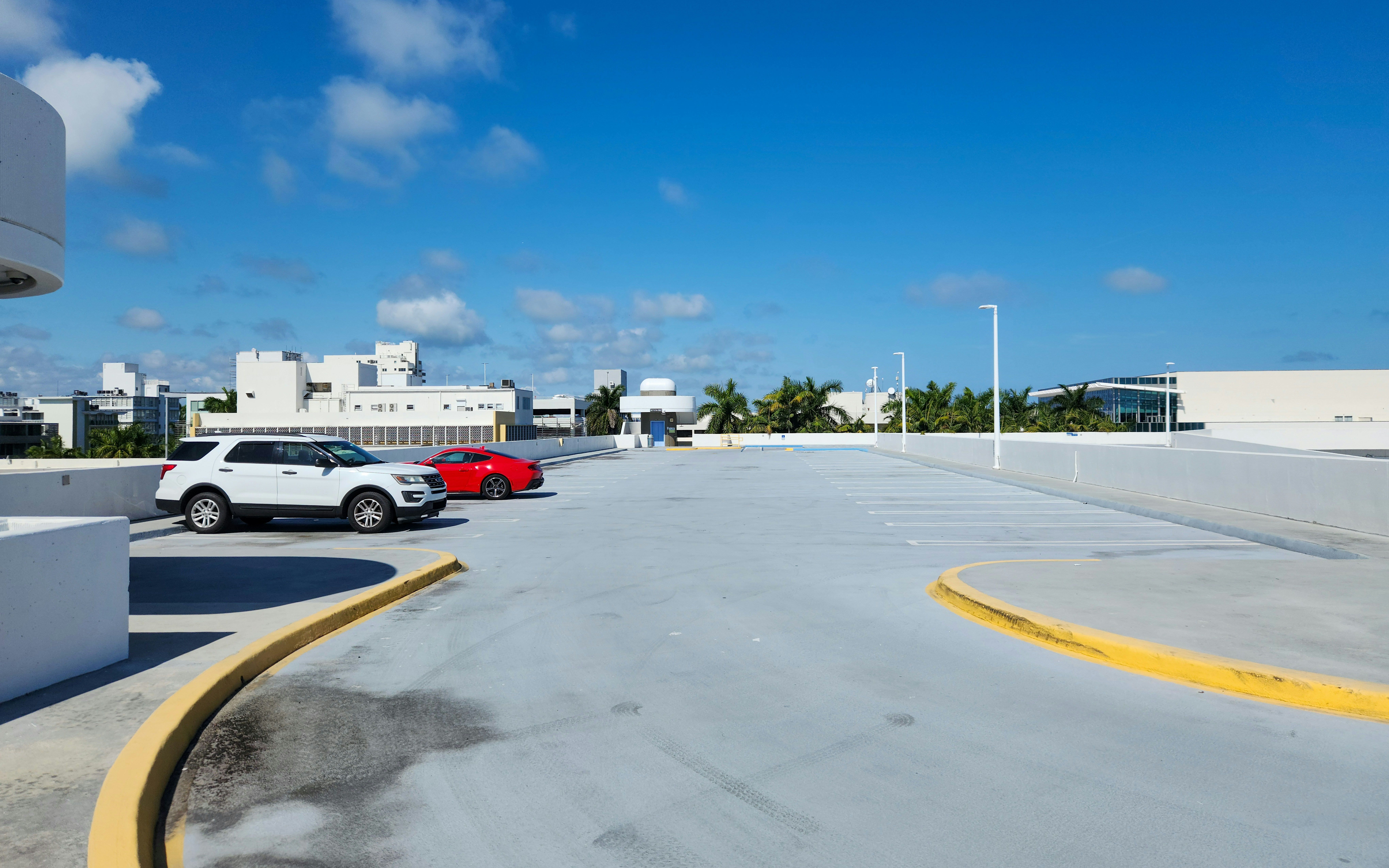 Empty rooftop parking with a red and white car under a clear blue sky.