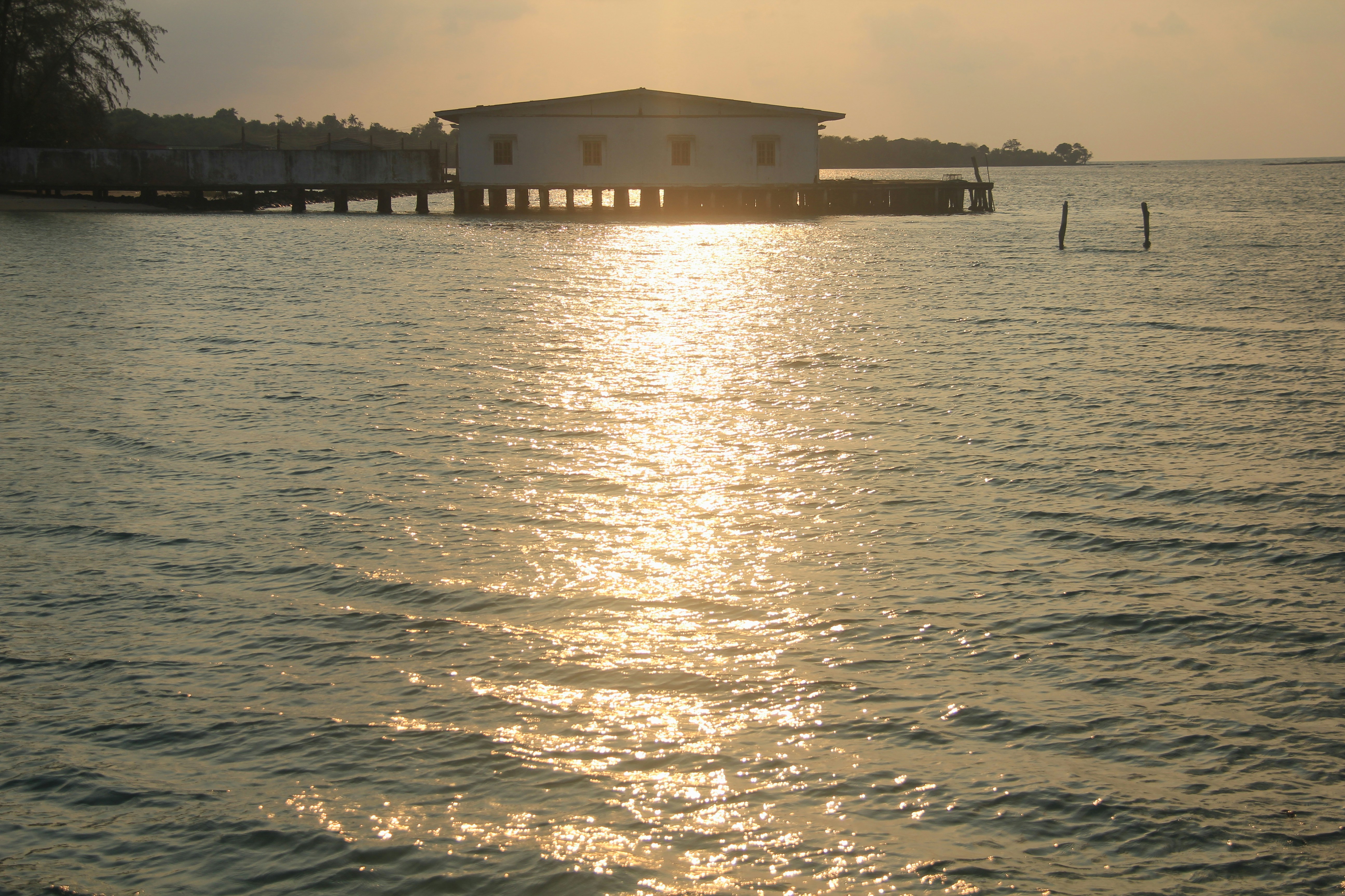 Sunset glow reflecting on rippling water near a solitary house on stilts.