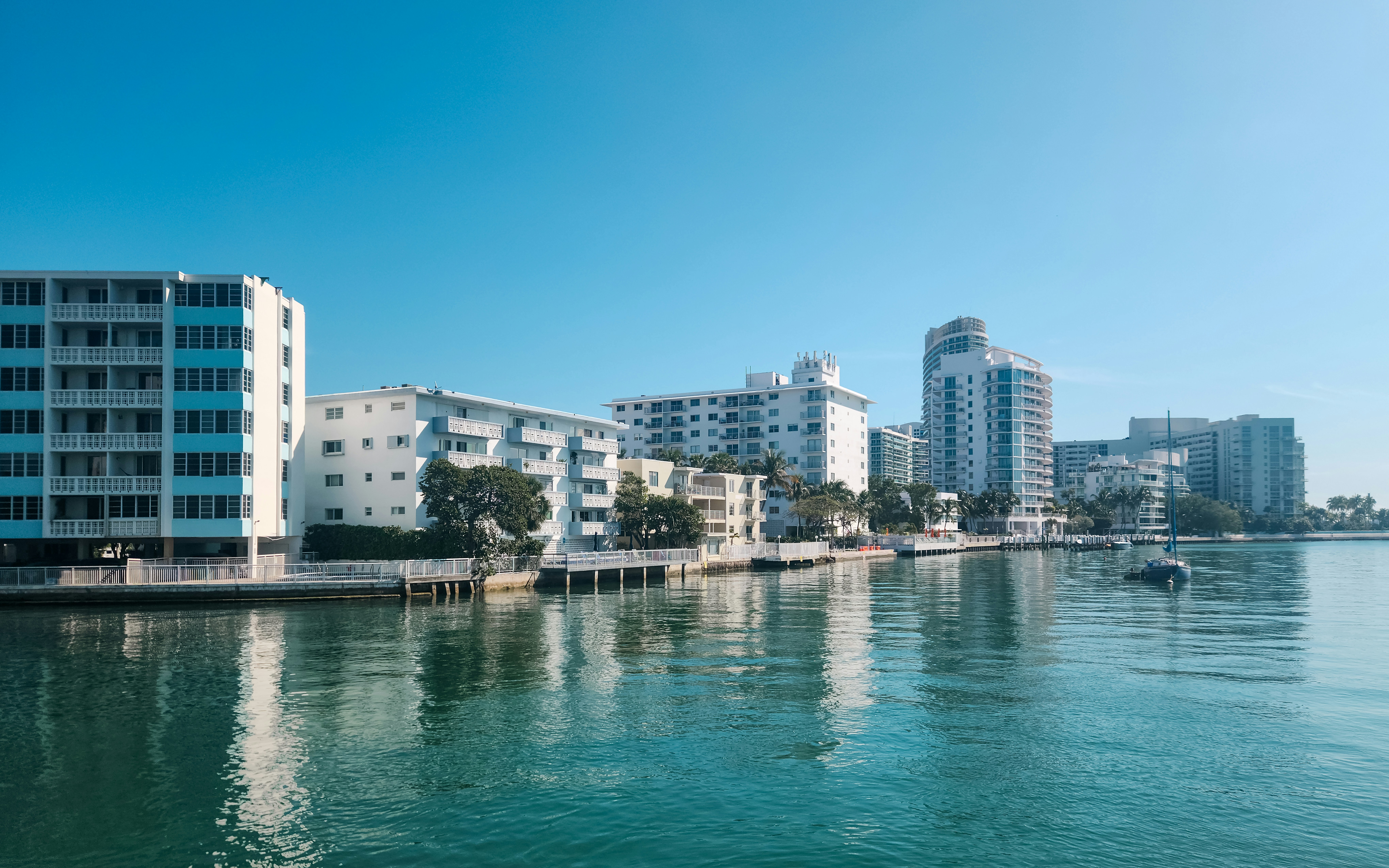 Modern buildings line the calm waters of Biscayne Bay under a clear blue sky.