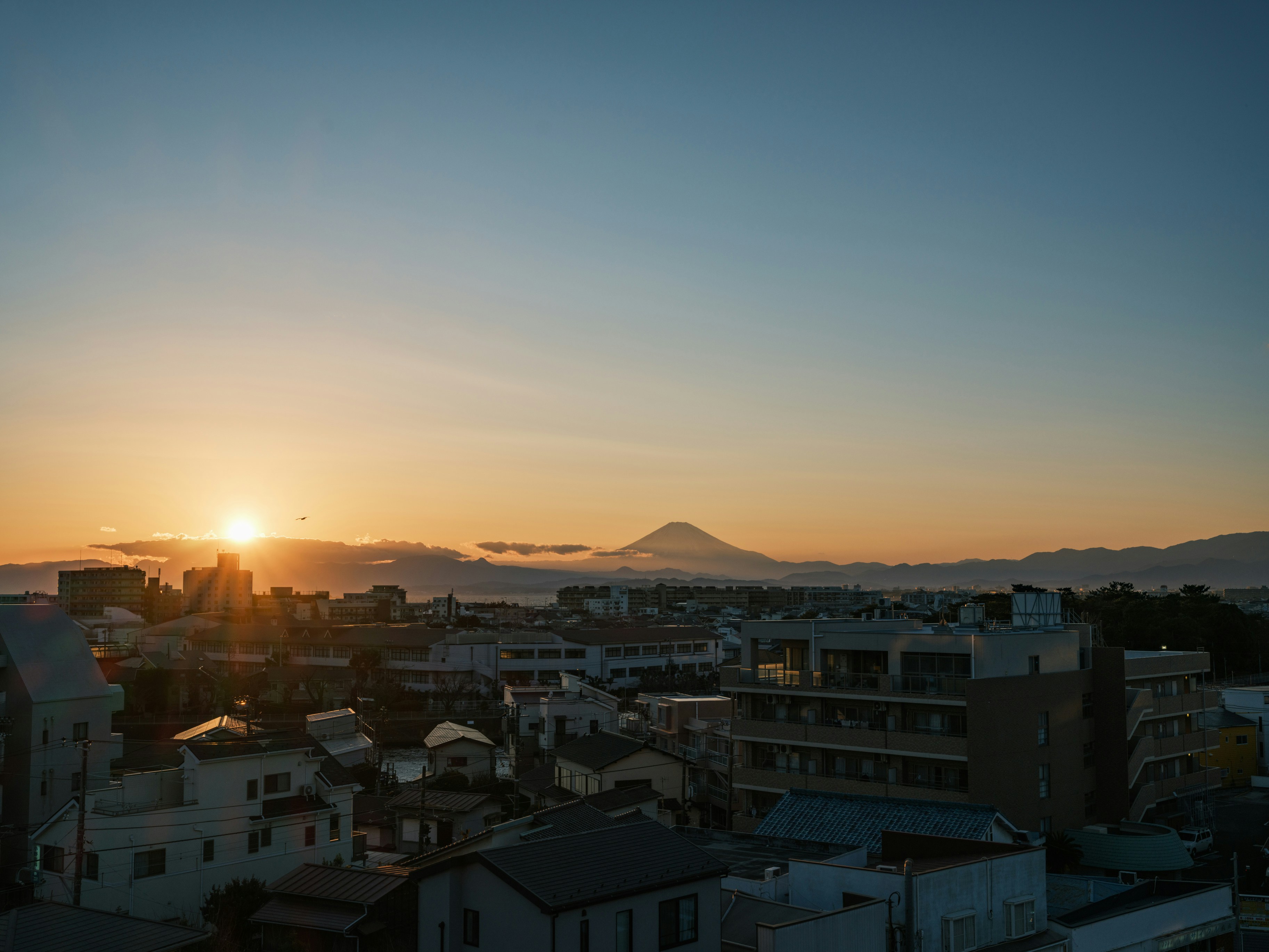 Sunset casting warm hues over a cityscape with distant mountains on the horizon.