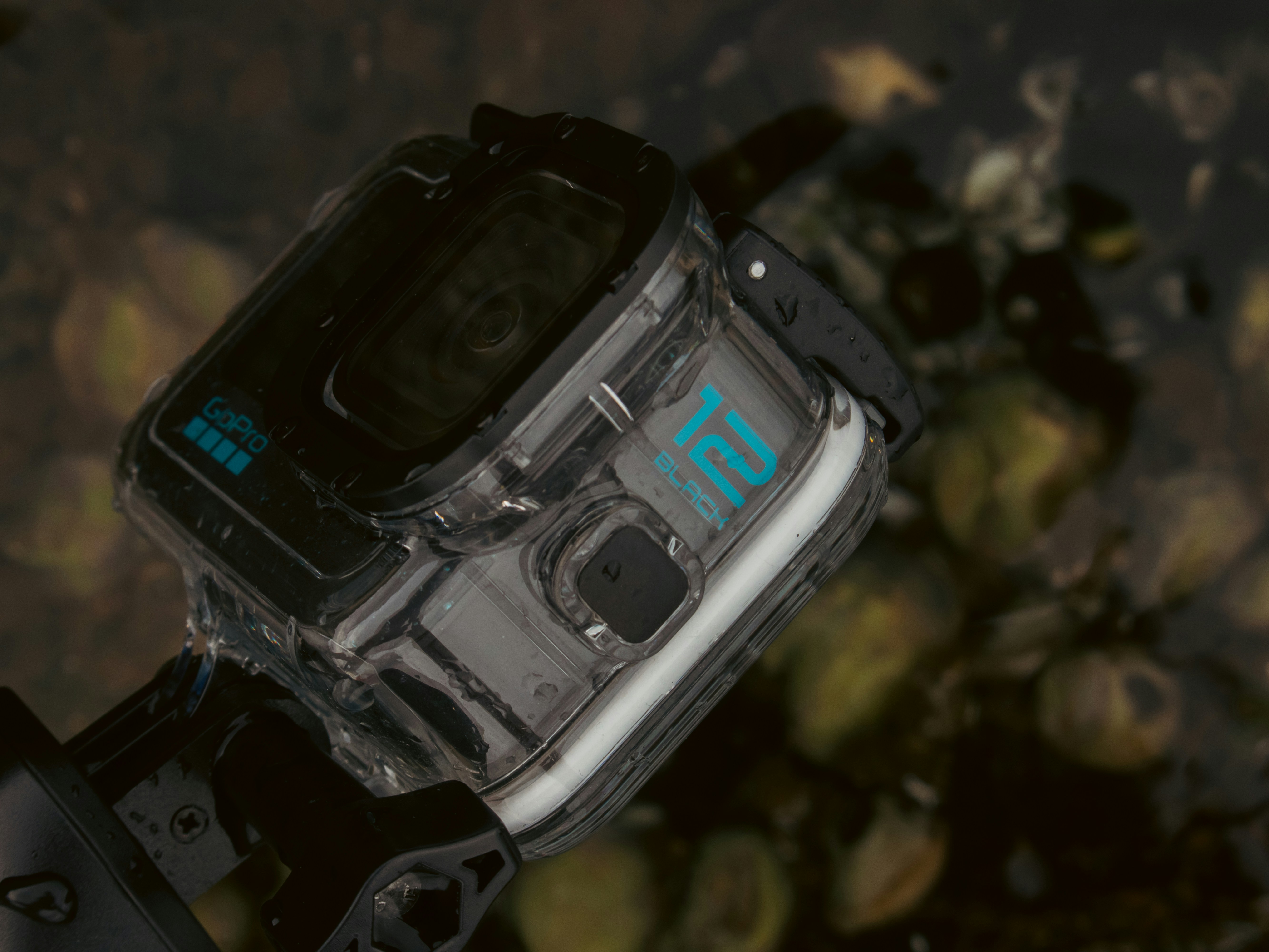 Close-up of a GoPro Hero 12 Black encased in a waterproof housing over a rocky waterbed.