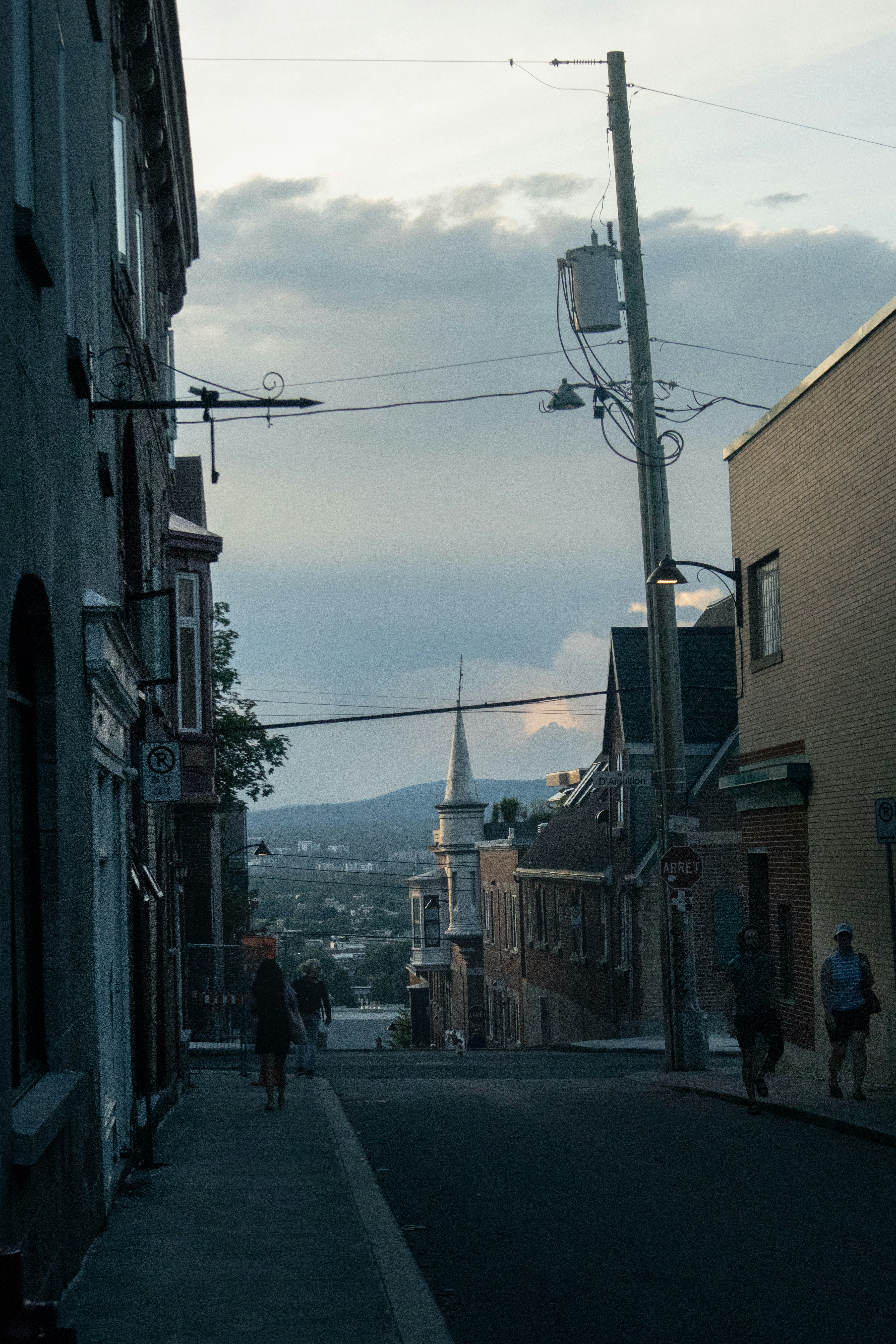 Narrow alleyway leading to a distant view of the Appalachian mountains at dusk with pedestrians walking by.