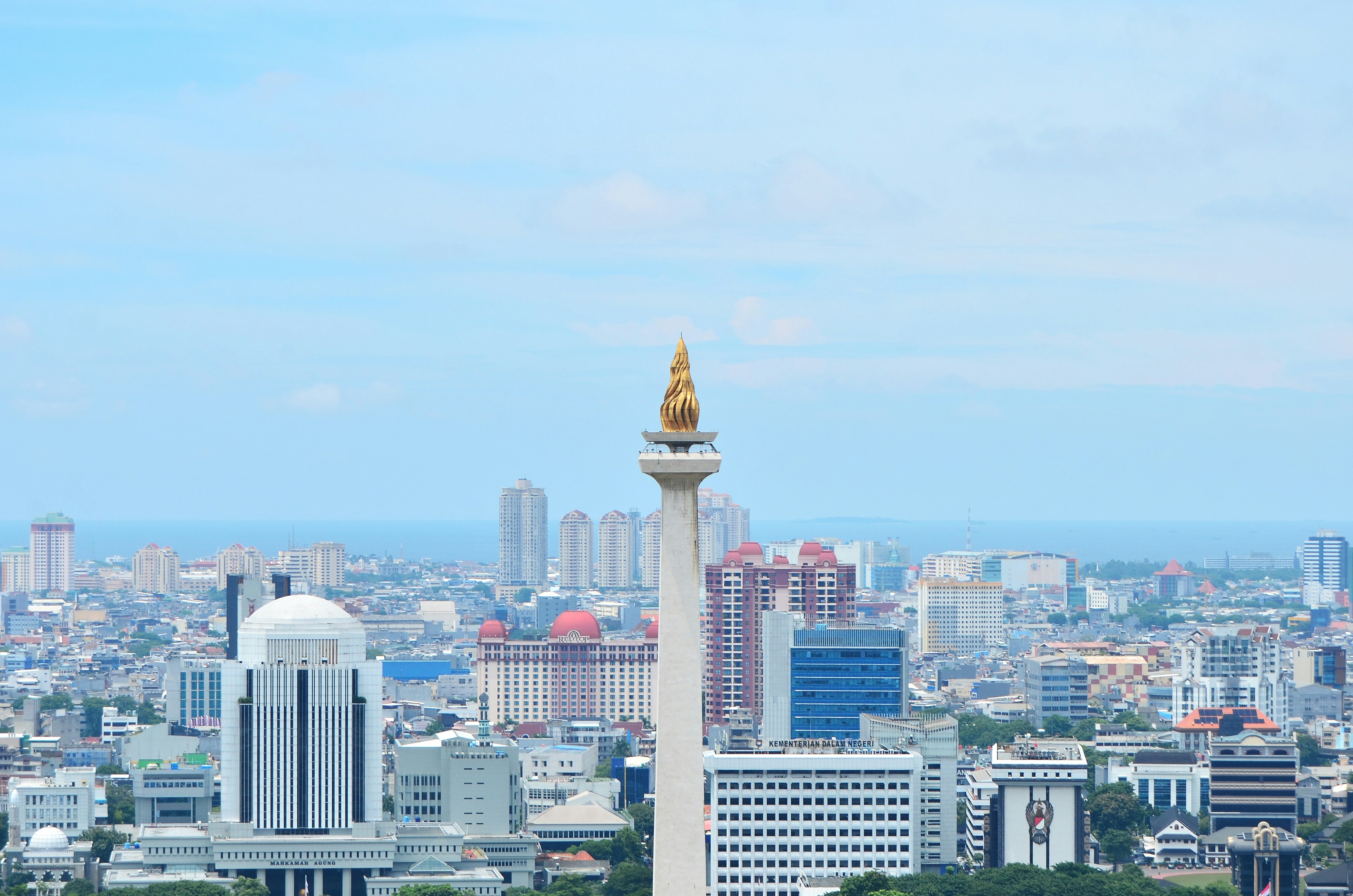 The National Monument rises above Jakarta's urban landscape under a clear blue sky.