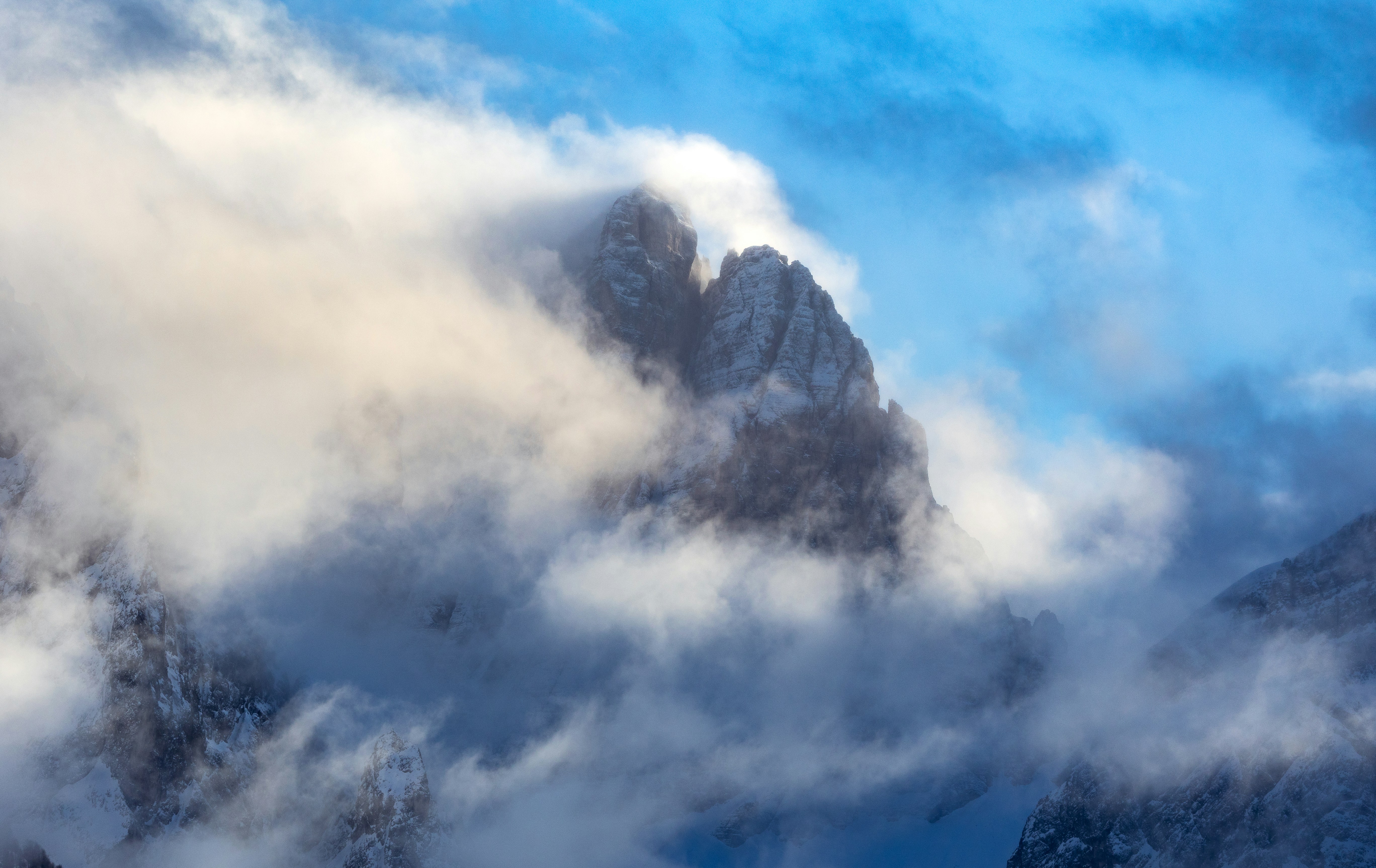Majestic mountain partially shrouded in swirling clouds under a blue sky.