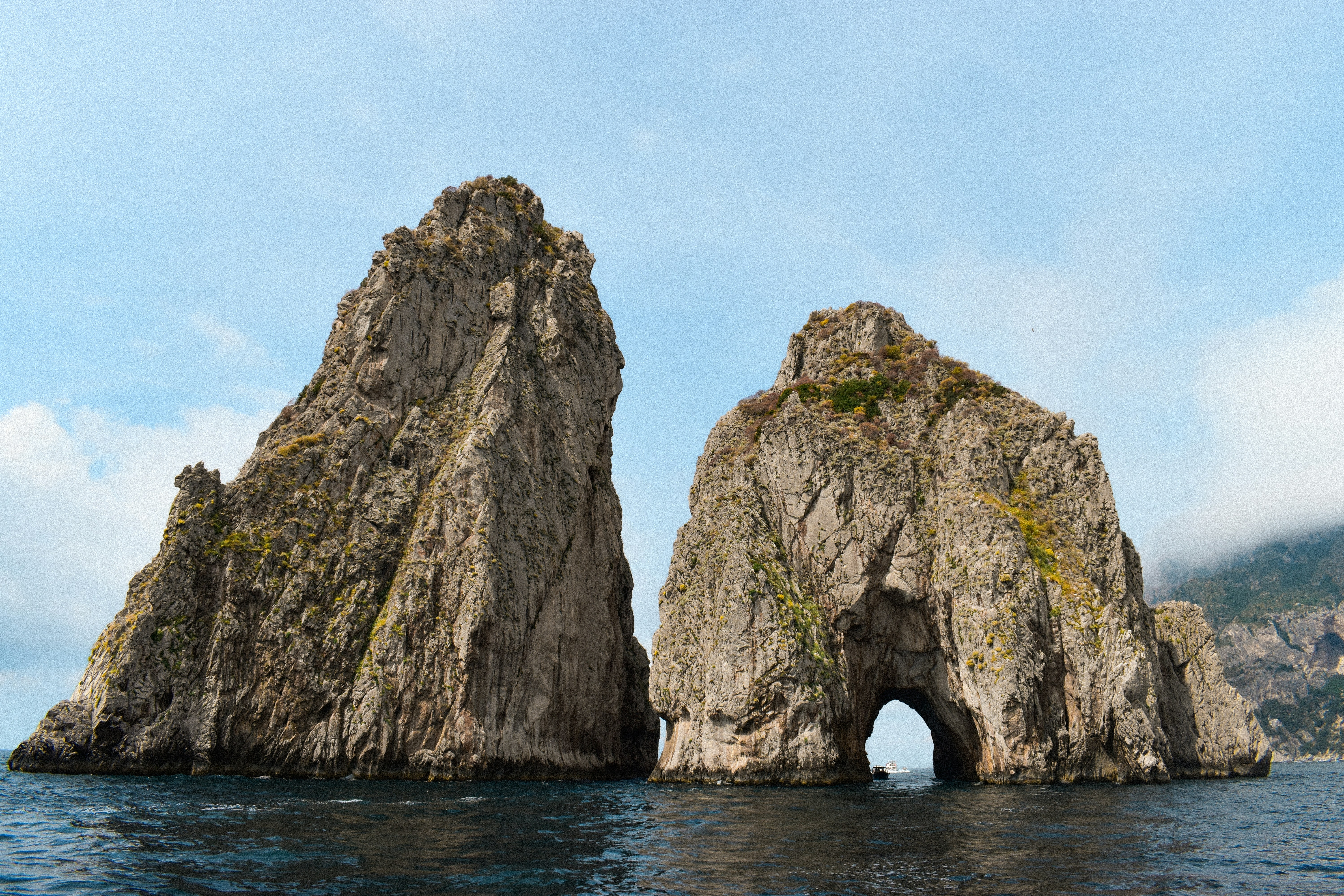 Towering rock formations rise from the sea under a clear blue sky.