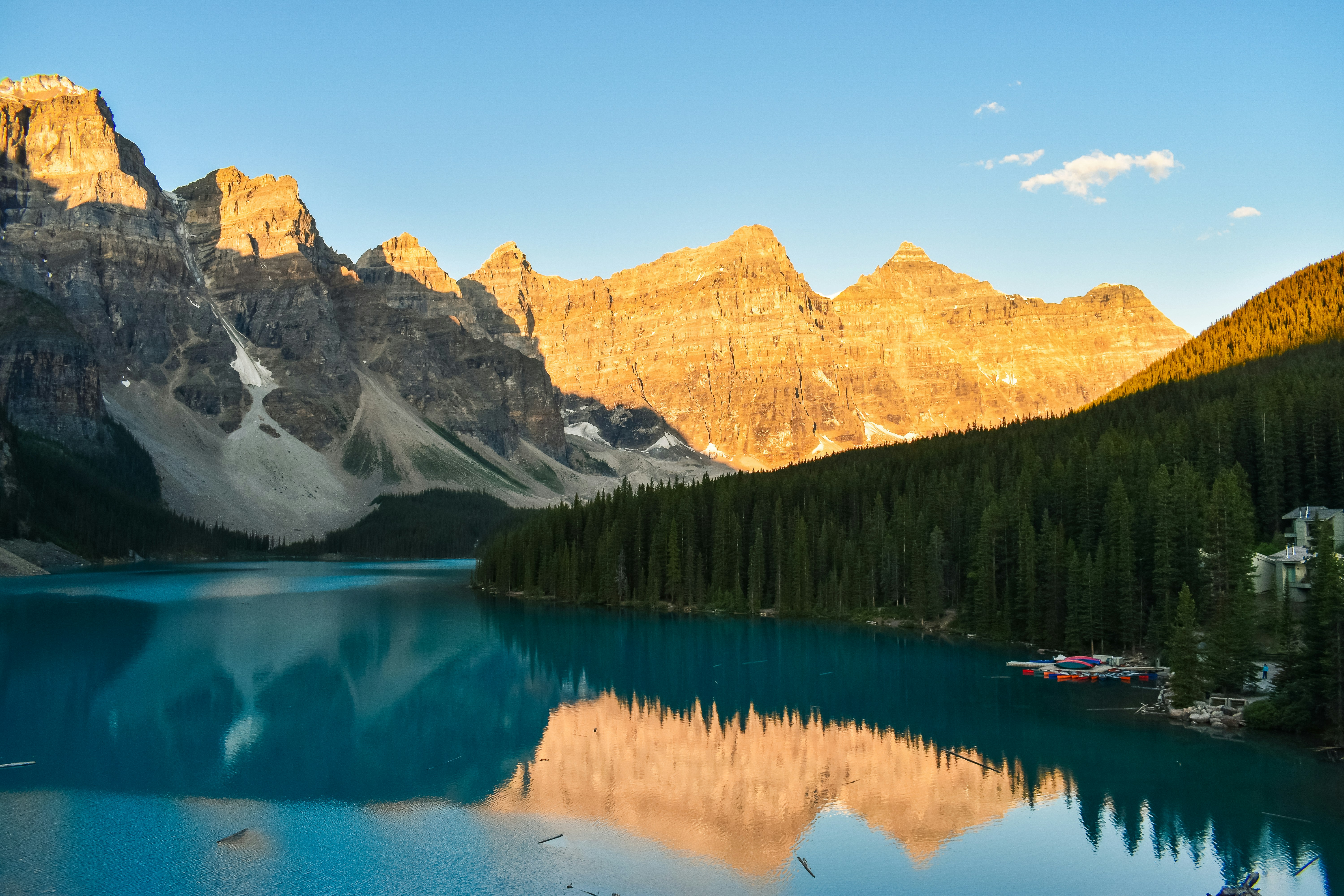 Sunlit mountain peaks mirrored in a serene blue lake surrounded by dense forest.