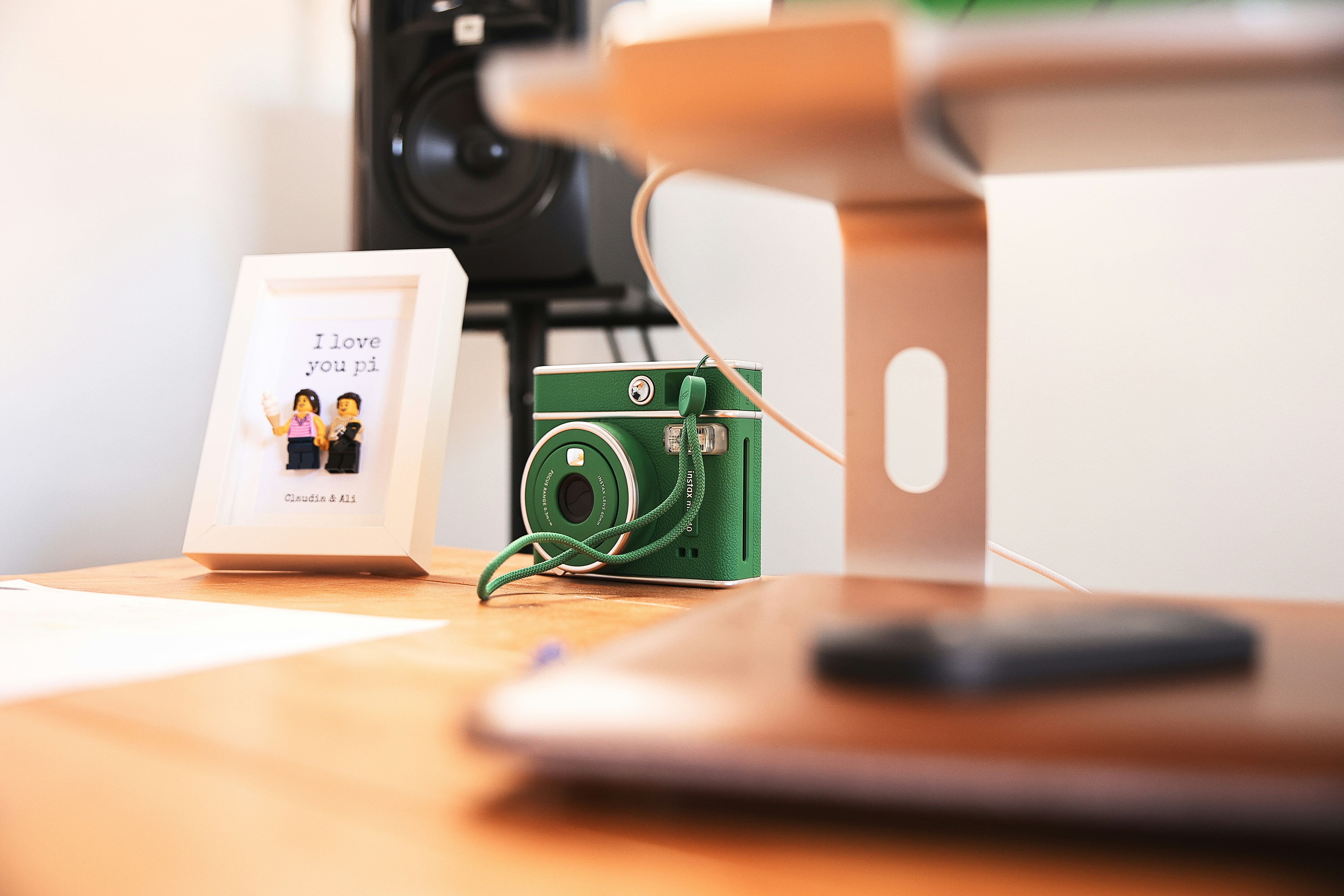 Green vintage-style camera and framed Lego artwork on a wooden desk.