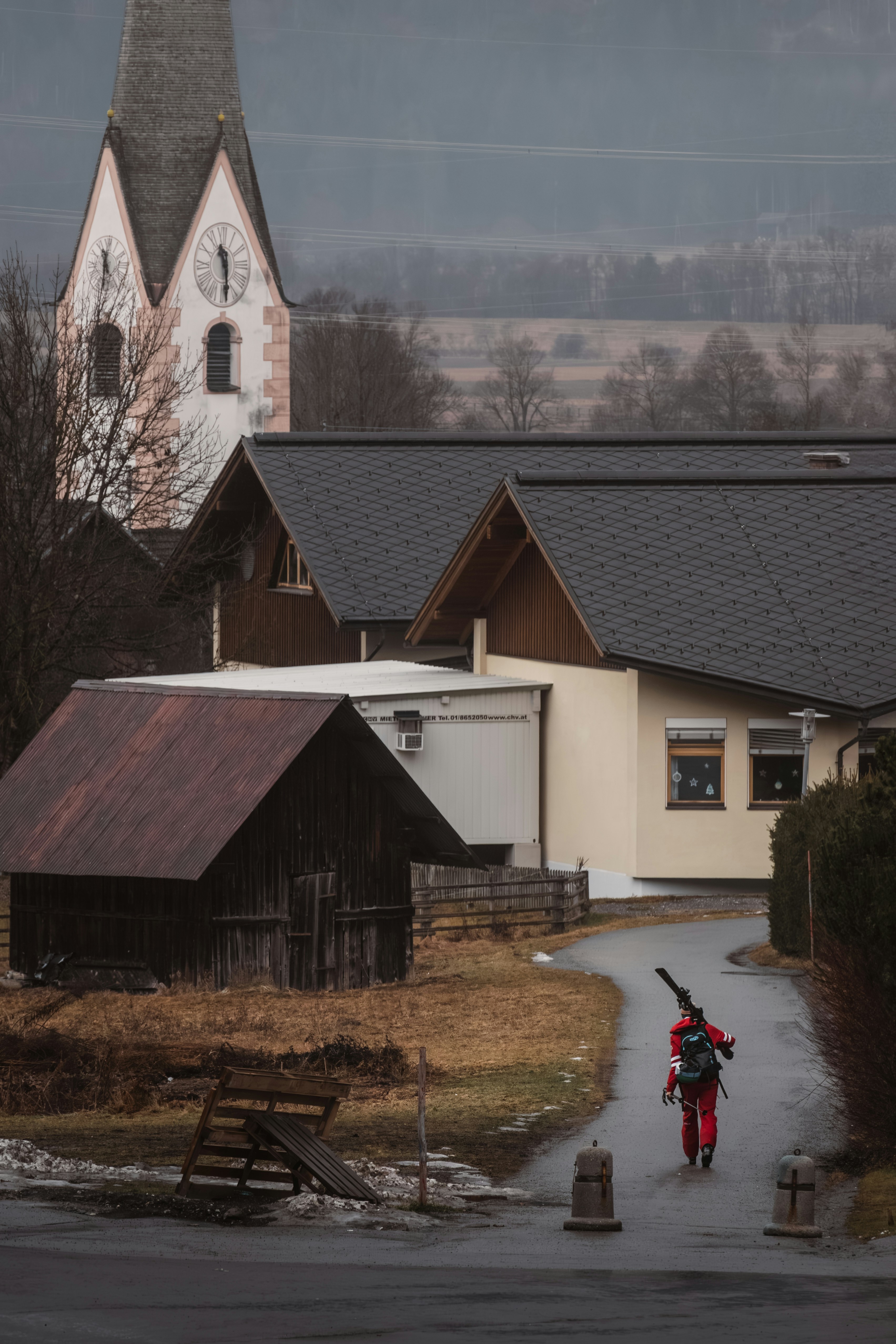 Red-clad traveler on a quiet winter village road toward the church tower