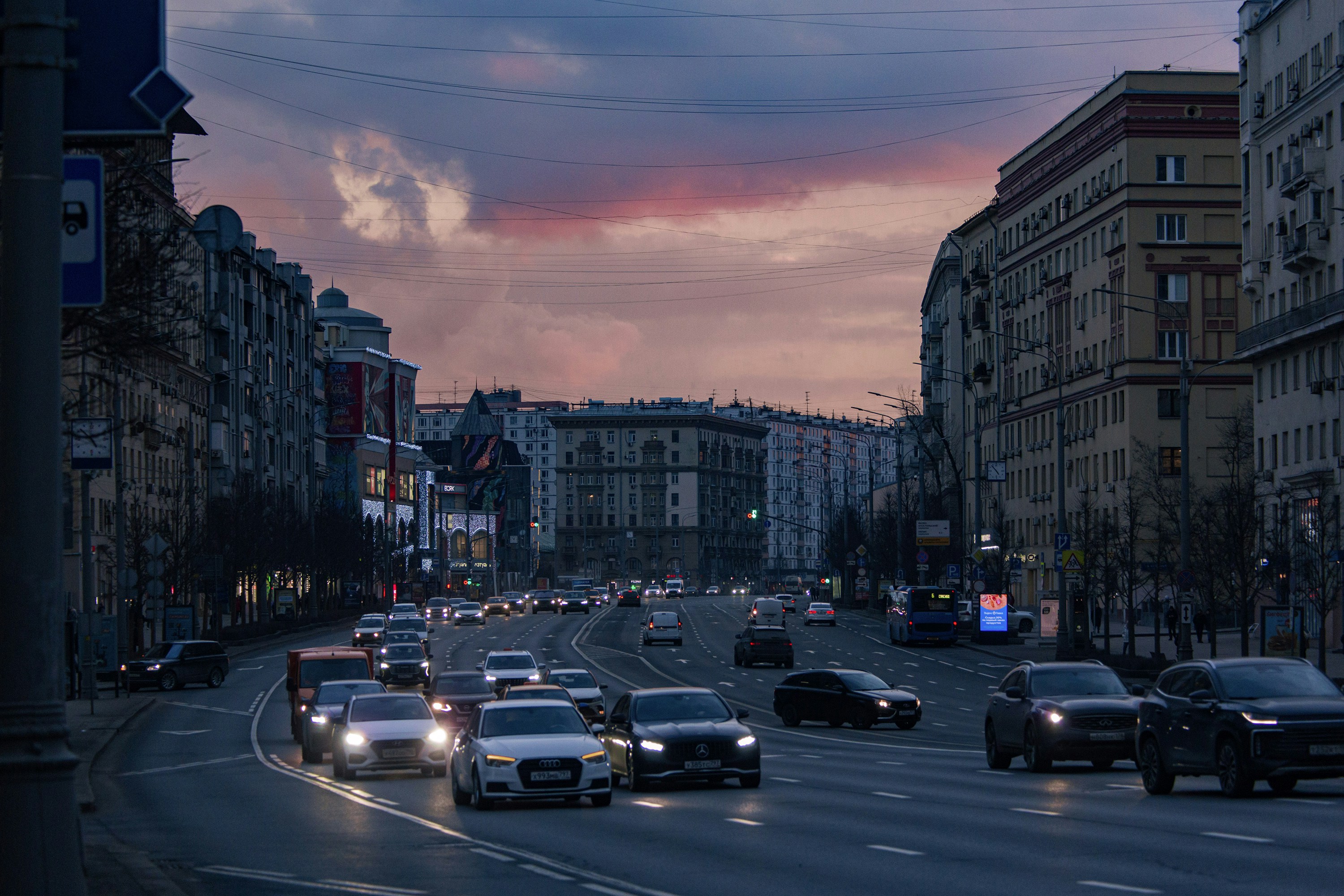 Evening traffic flows through a city street under a vibrant sunset sky.