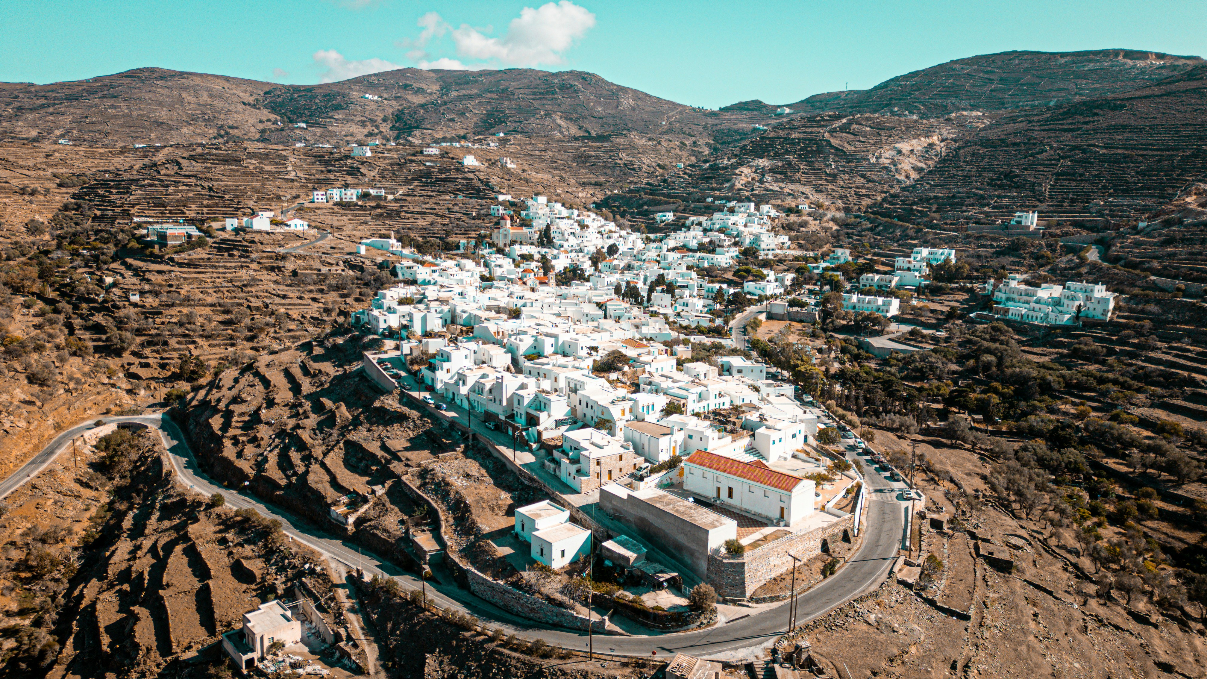 Cluster of white buildings nestled in the rugged hills of Tinos Island under a clear sky.