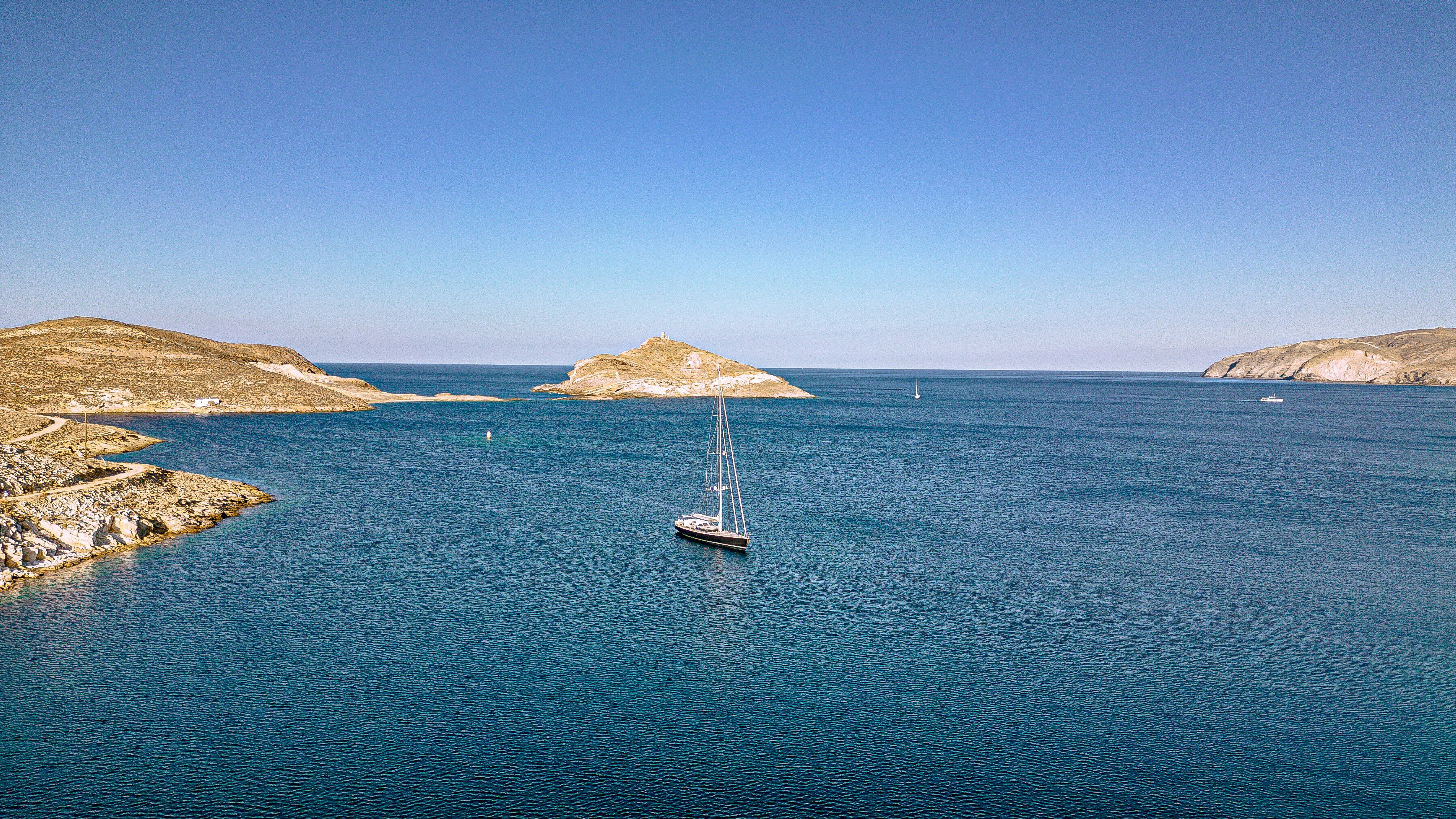 Sailboat gliding through the calm waters near rocky shores of Tinos Island under a clear sky.