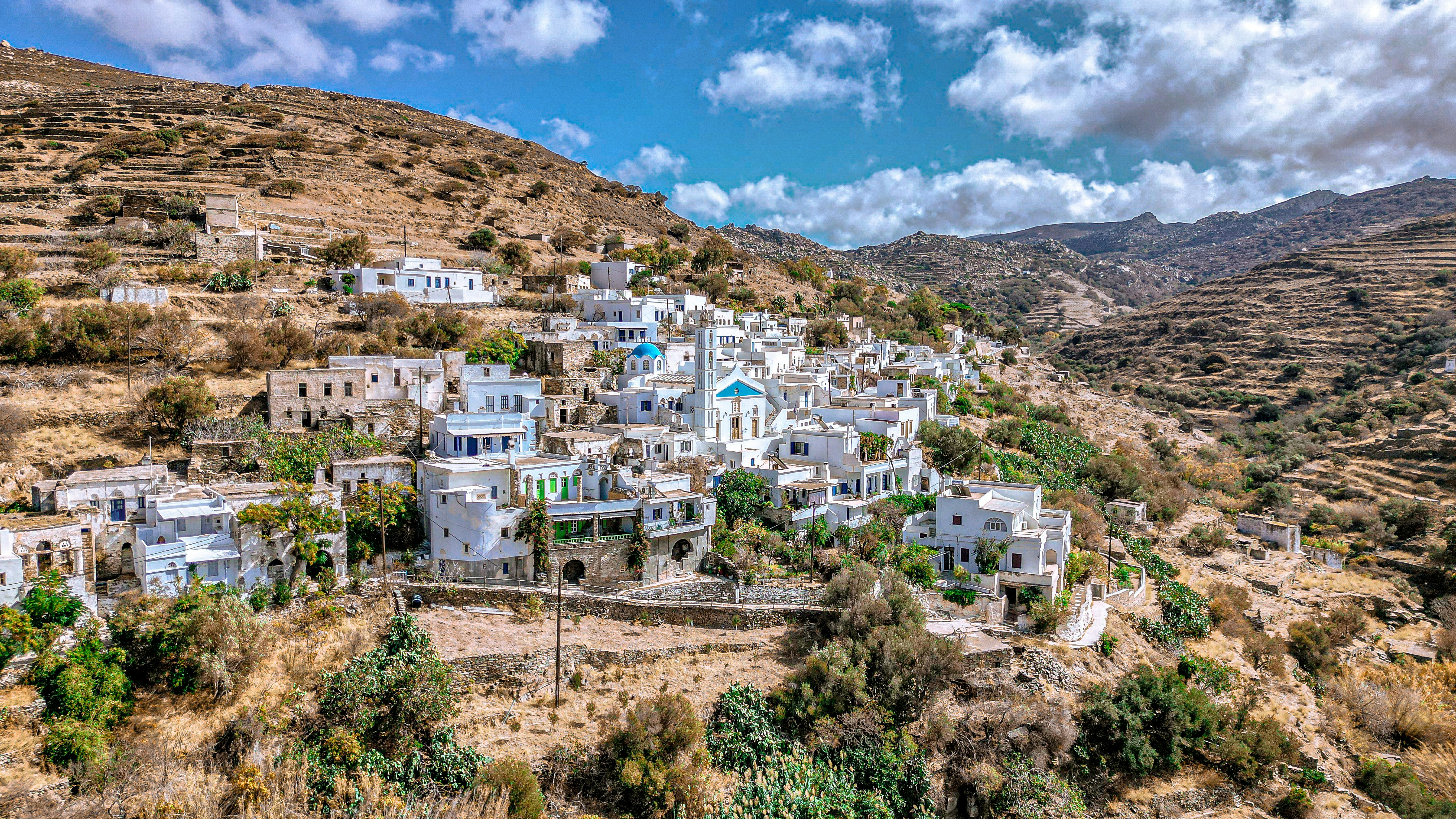 Whitewashed buildings nestled in the terraced hills of Tinos under a vibrant sky.