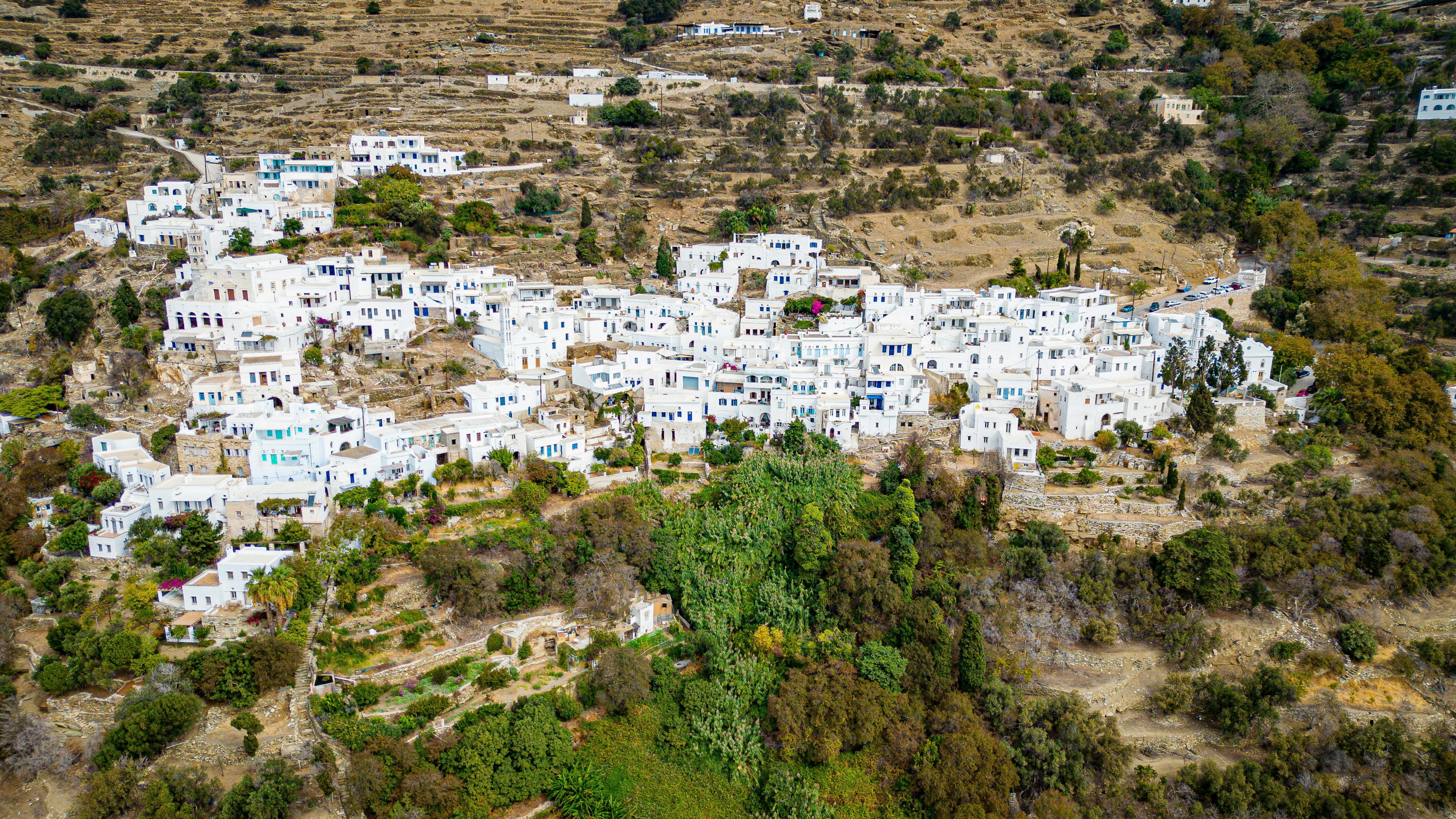 Cluster of white buildings nestled in the terraced landscape of Tinos Island.