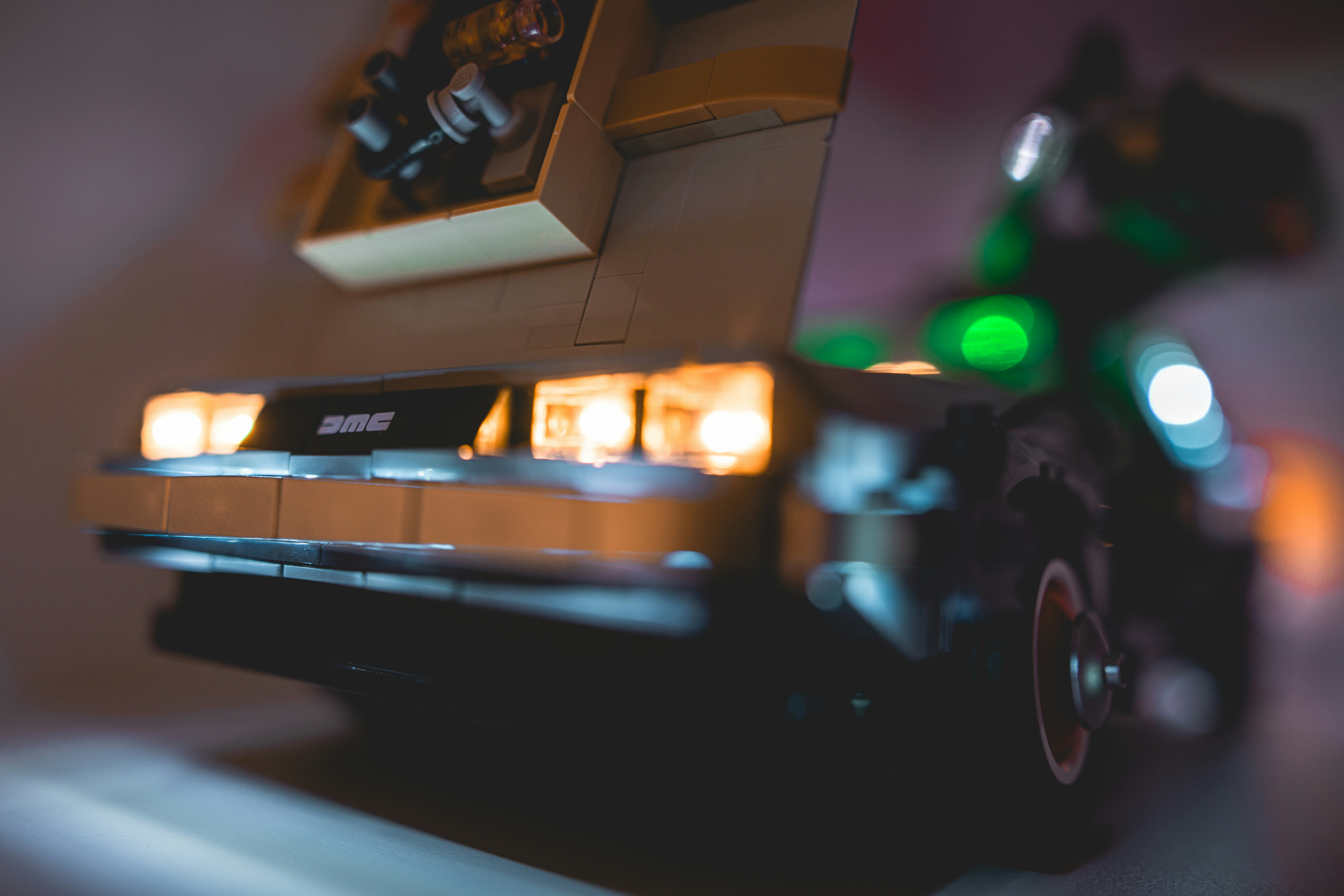 Close-up of a detailed LEGO model car with illuminated headlights and blurred background.
