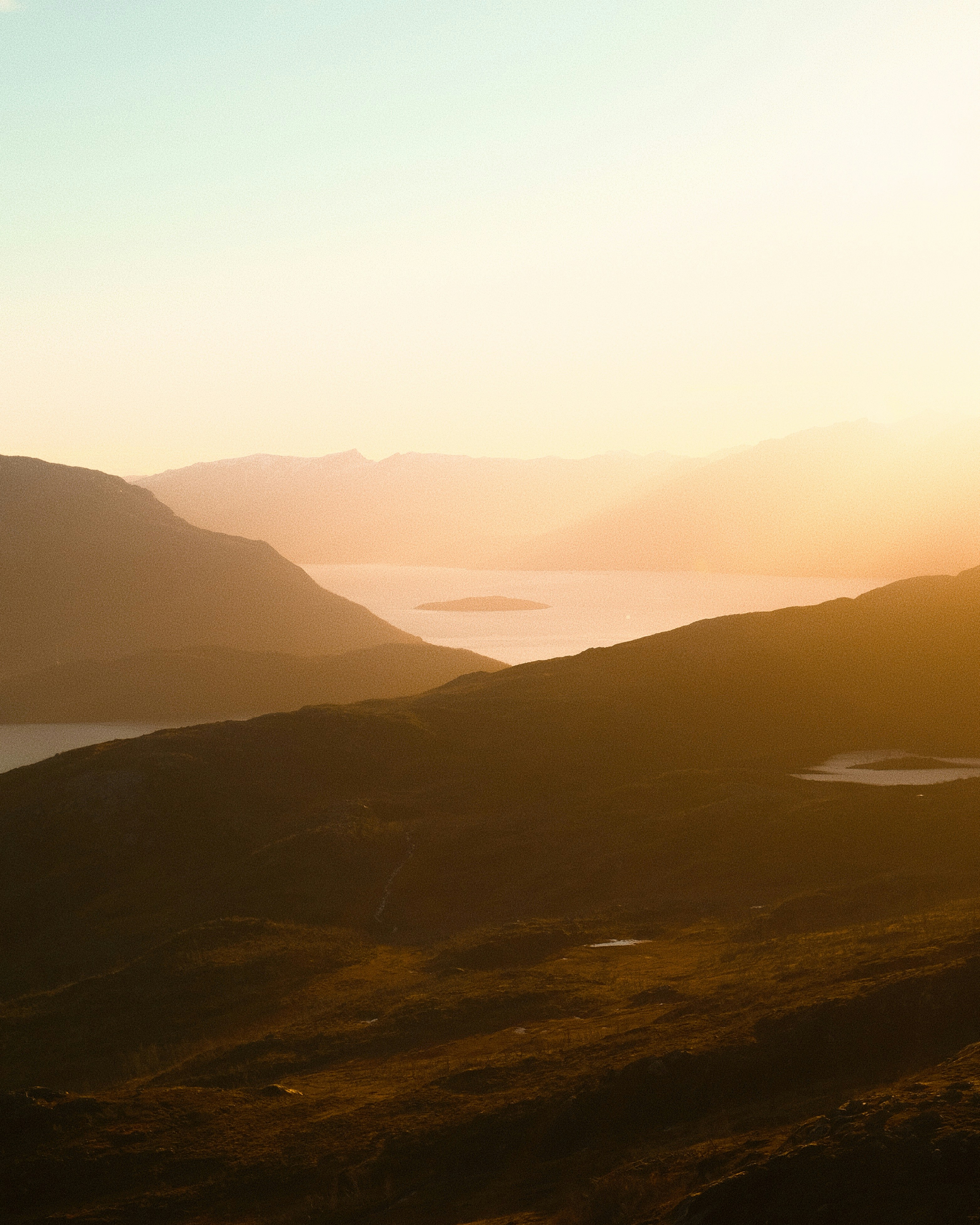 Serene landscape at sunset, showcasing rolling hills and distant islands bathed in golden light.