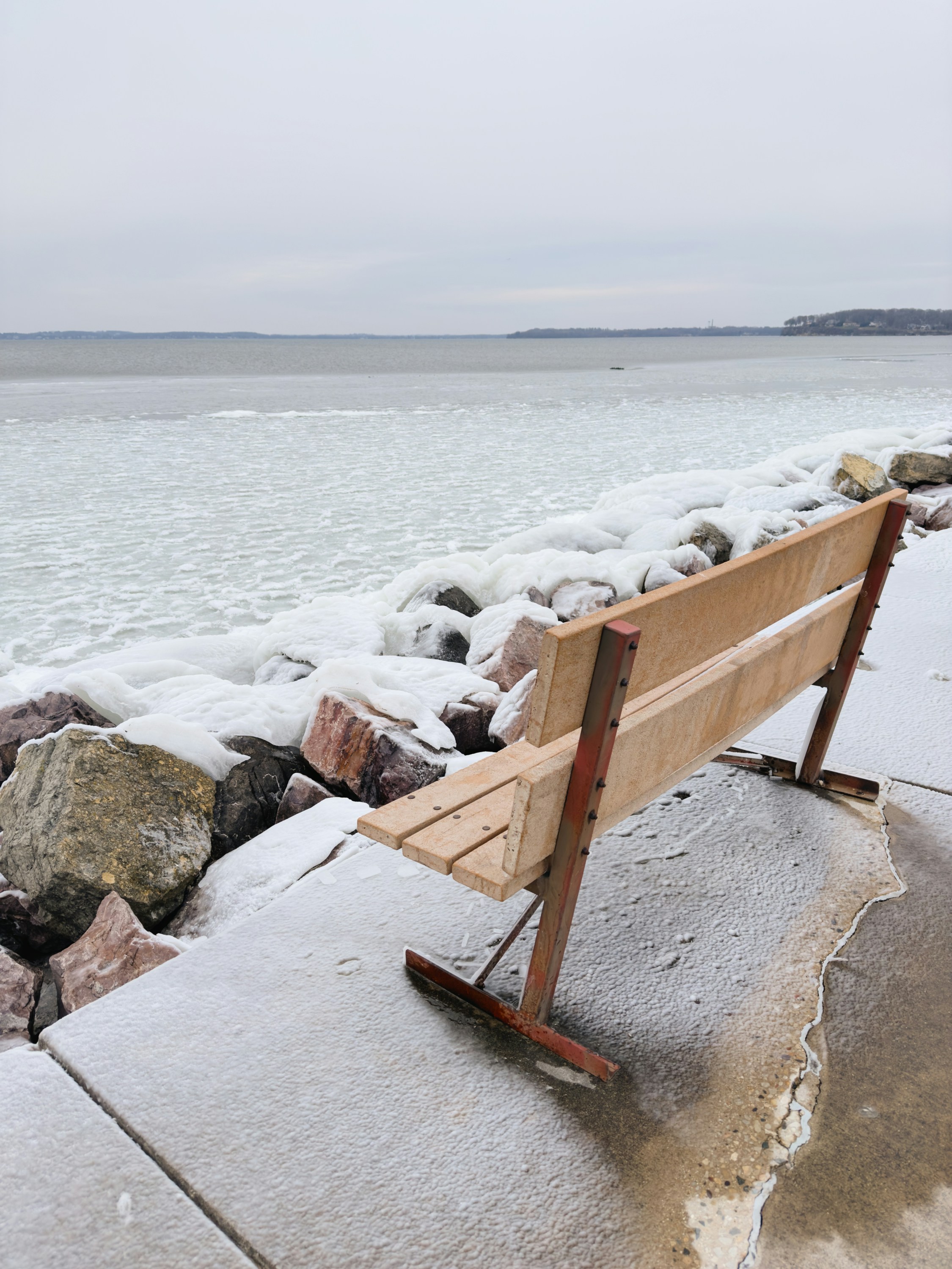 Snow-kissed shoreline bench facing a quiet winter horizon