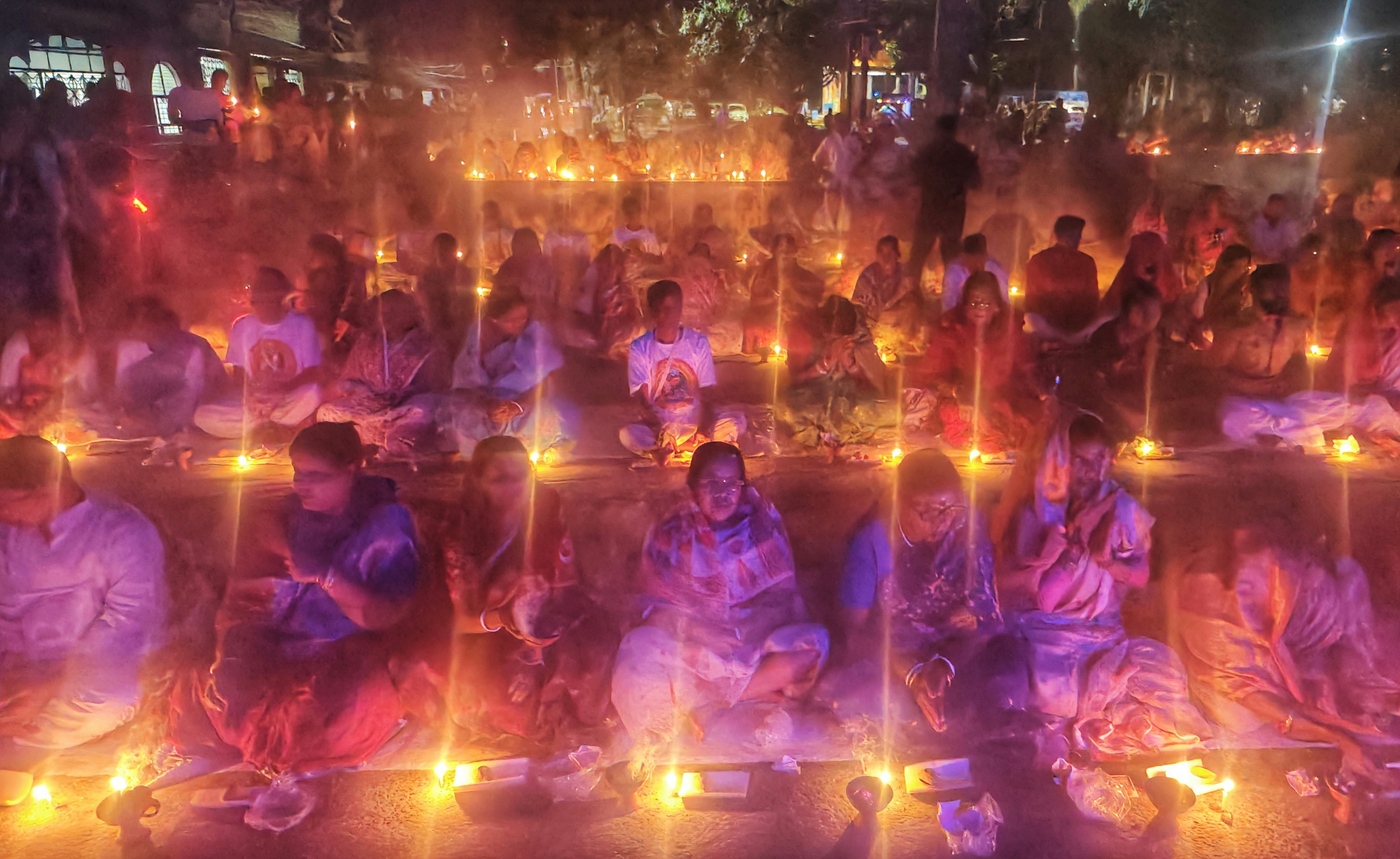 Candlelit crowd at night, faces illuminated by torches against a hazy orange glow.