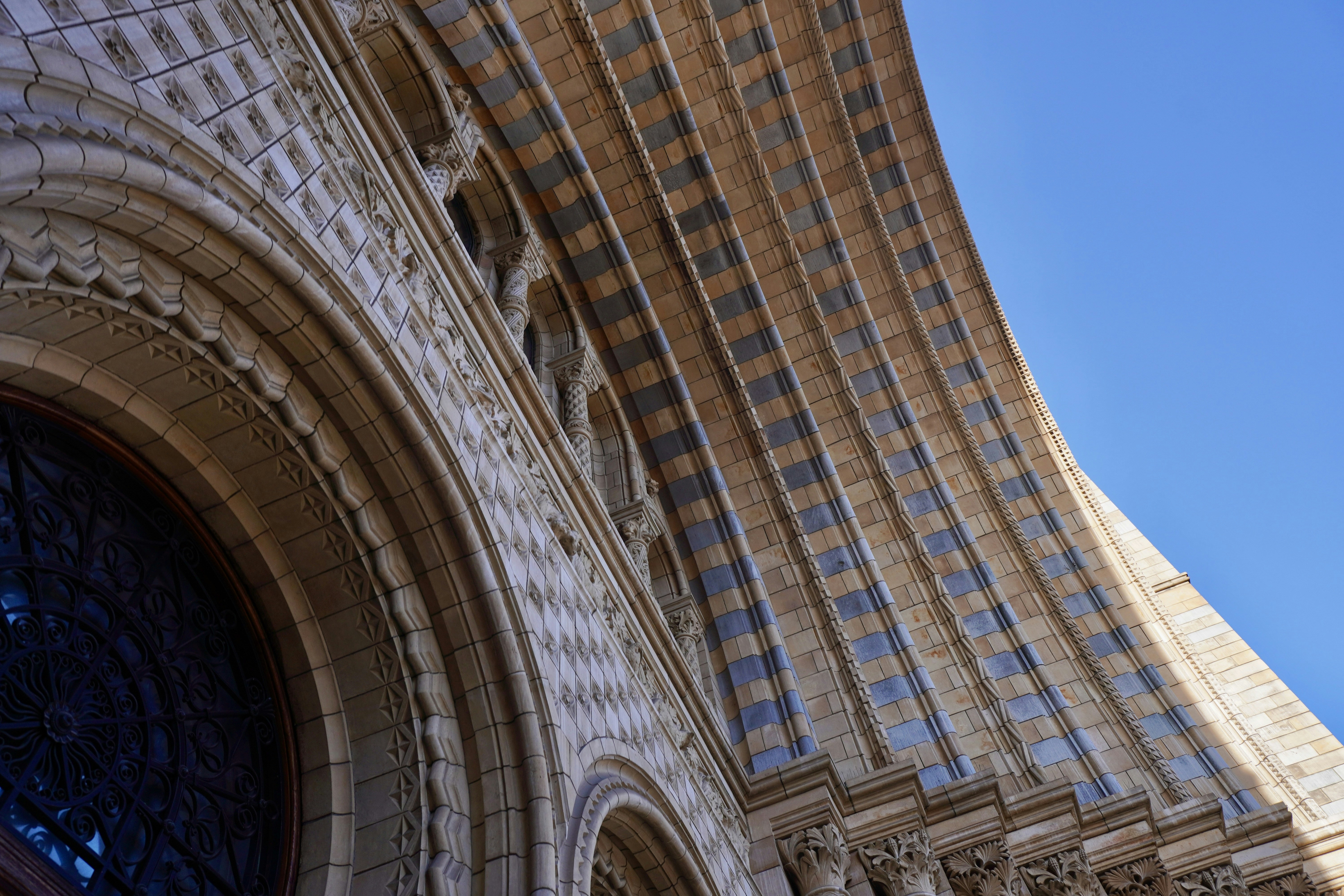 Intricate stonework and terracotta tiles adorn the entrance of London's Natural History Museum beneath a clear blue sky.