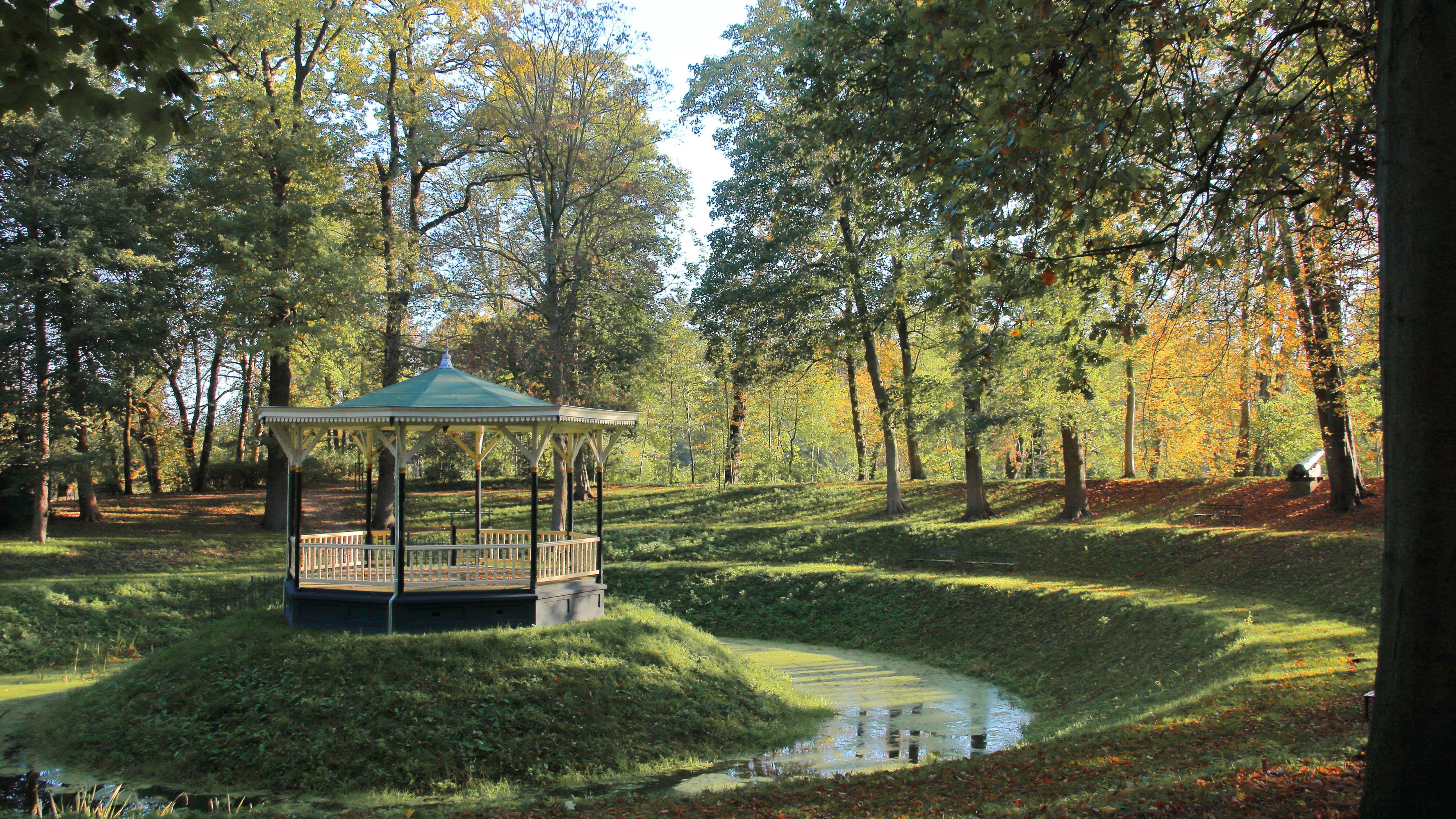 A tranquil gazebo nestled in a sunlit park surrounded by autumn trees.