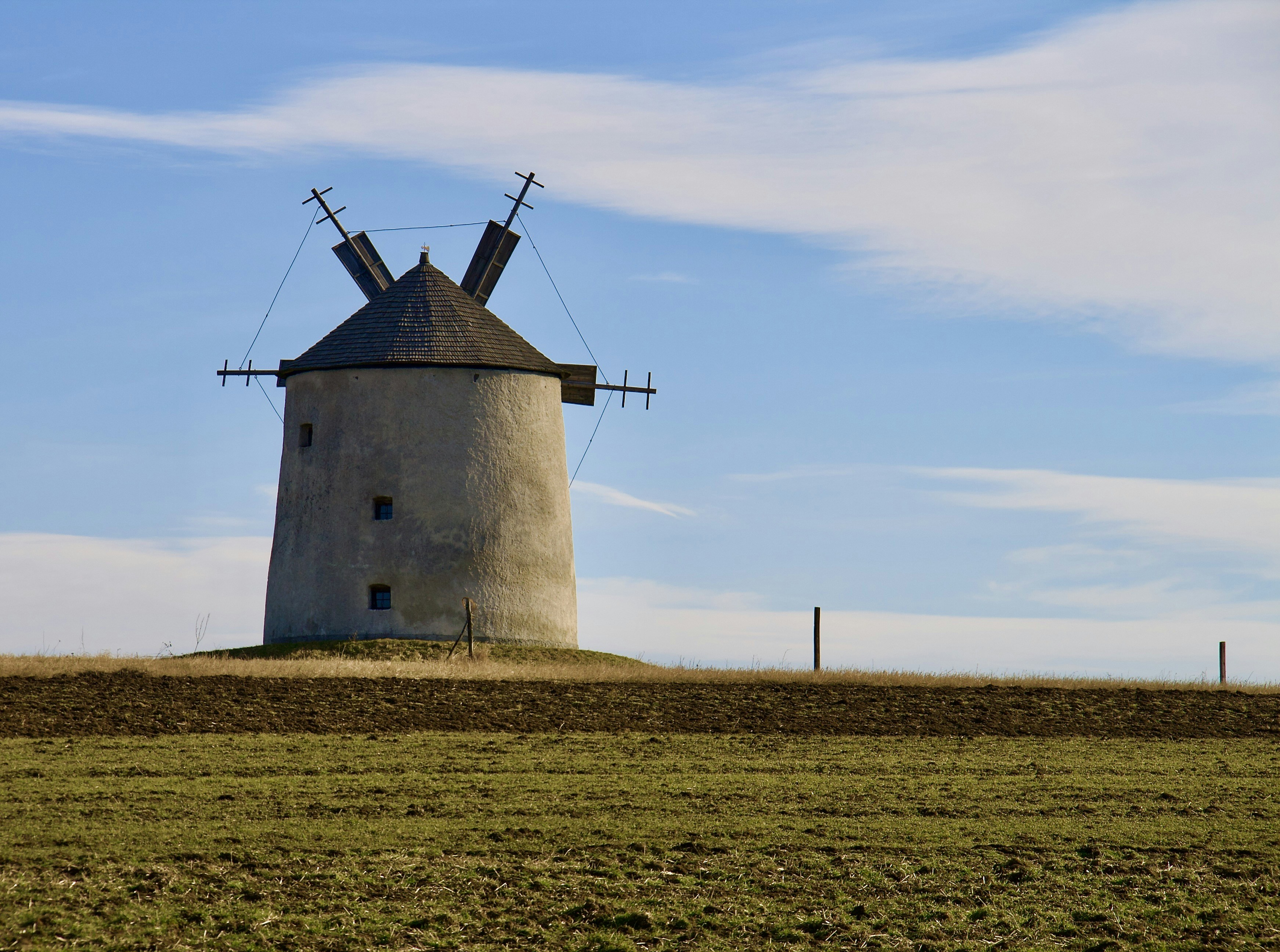 Historic windmill stands alone in a grassy field against a blue sky.
