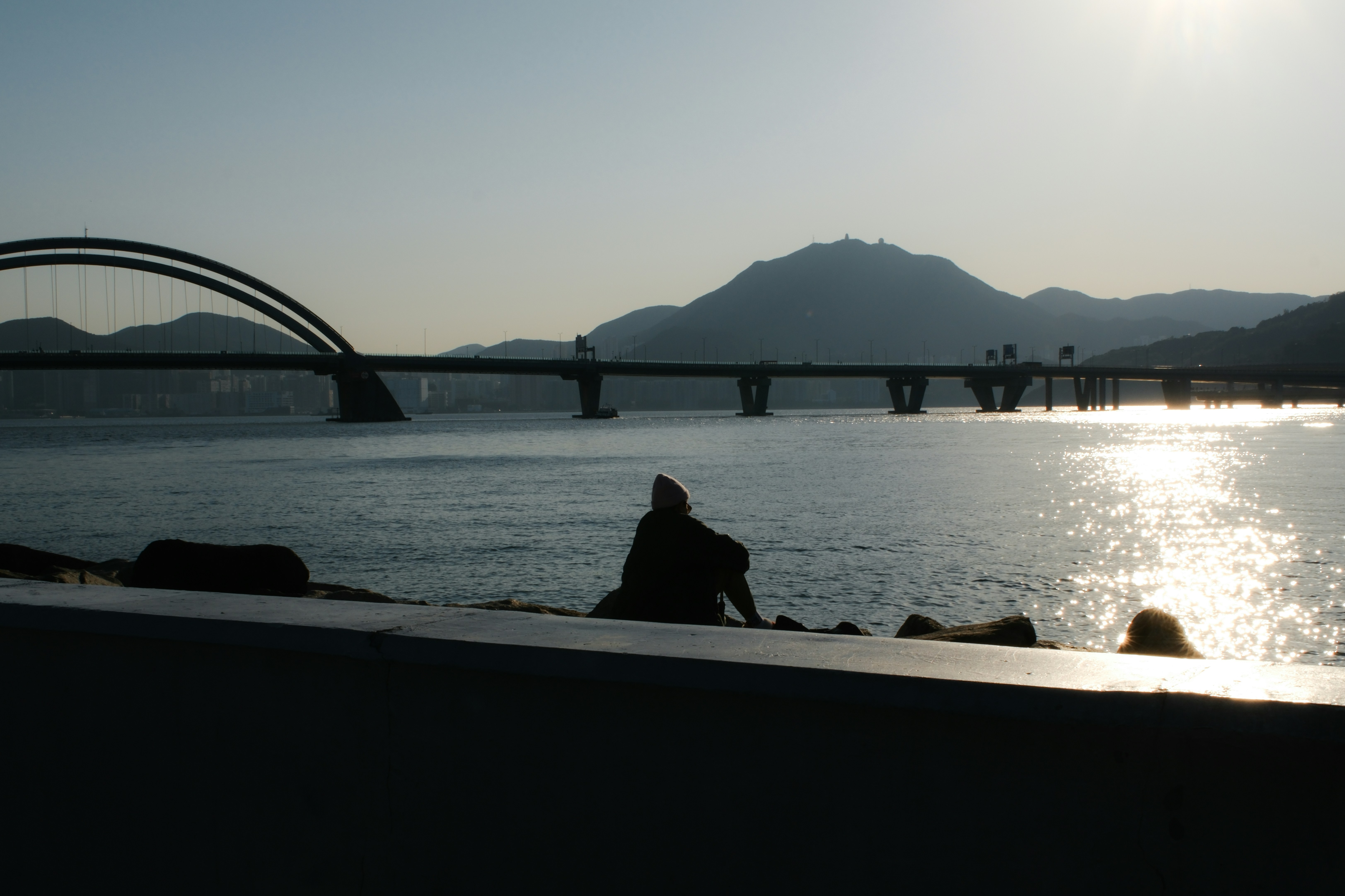 A person sitting on a ledge looking out over a body of water photo ...