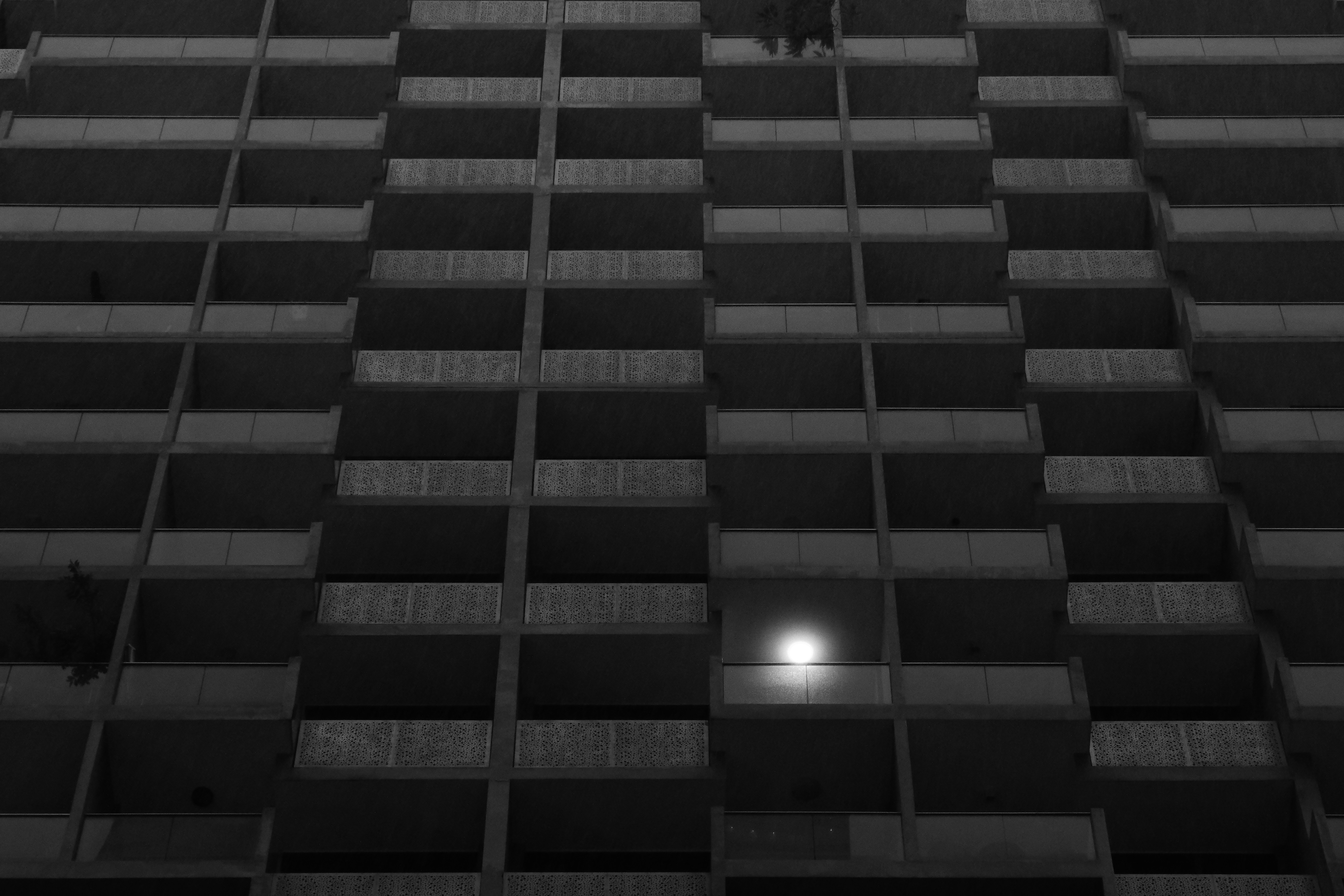 Symmetrical building facade with a single lit balcony in the center, creating a focal point amid darkness.