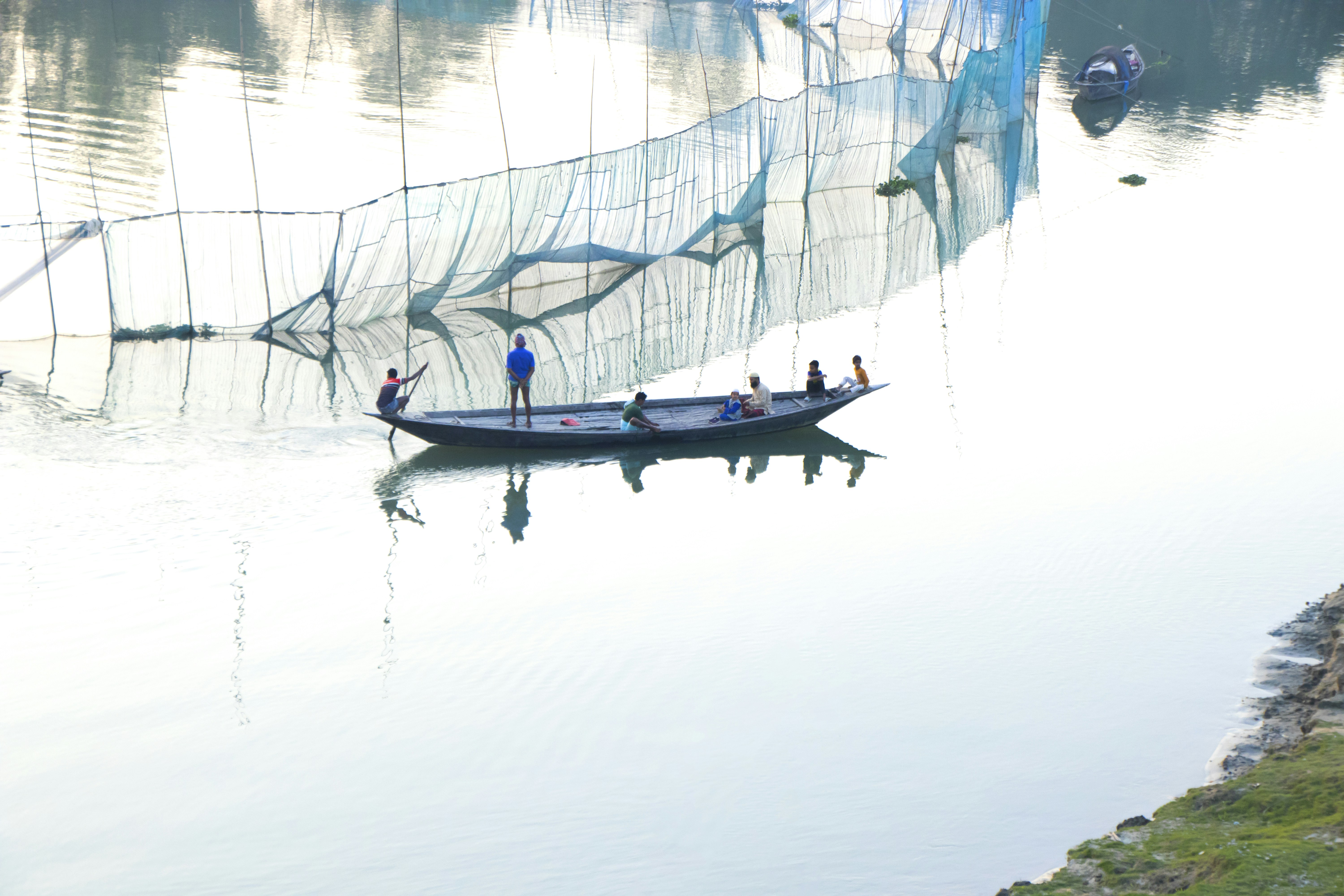 Fishermen on a boat beneath large, suspended fishing nets reflecting in calm water.