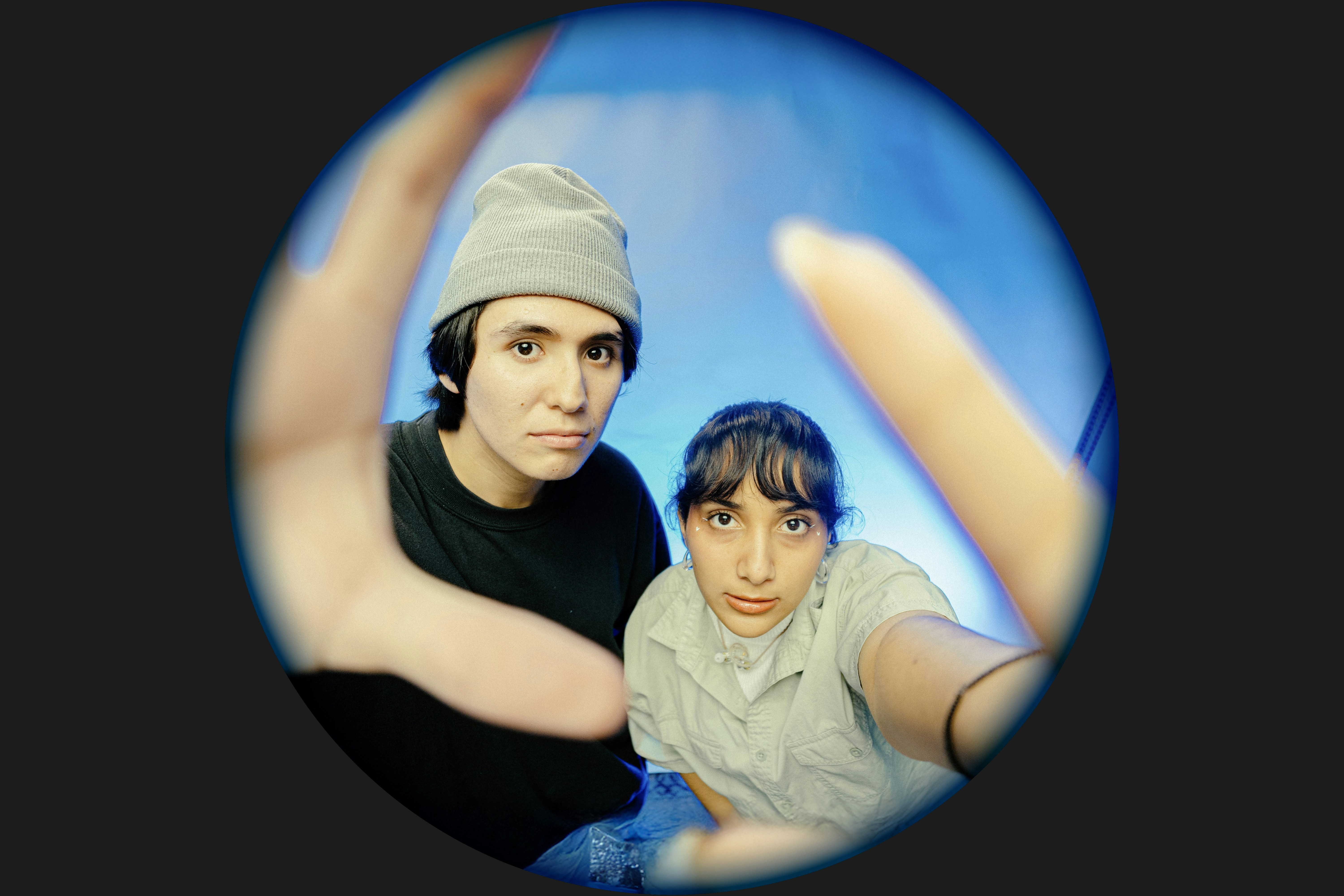 Two individuals framed by outstretched fingers, set against a vibrant blue background.