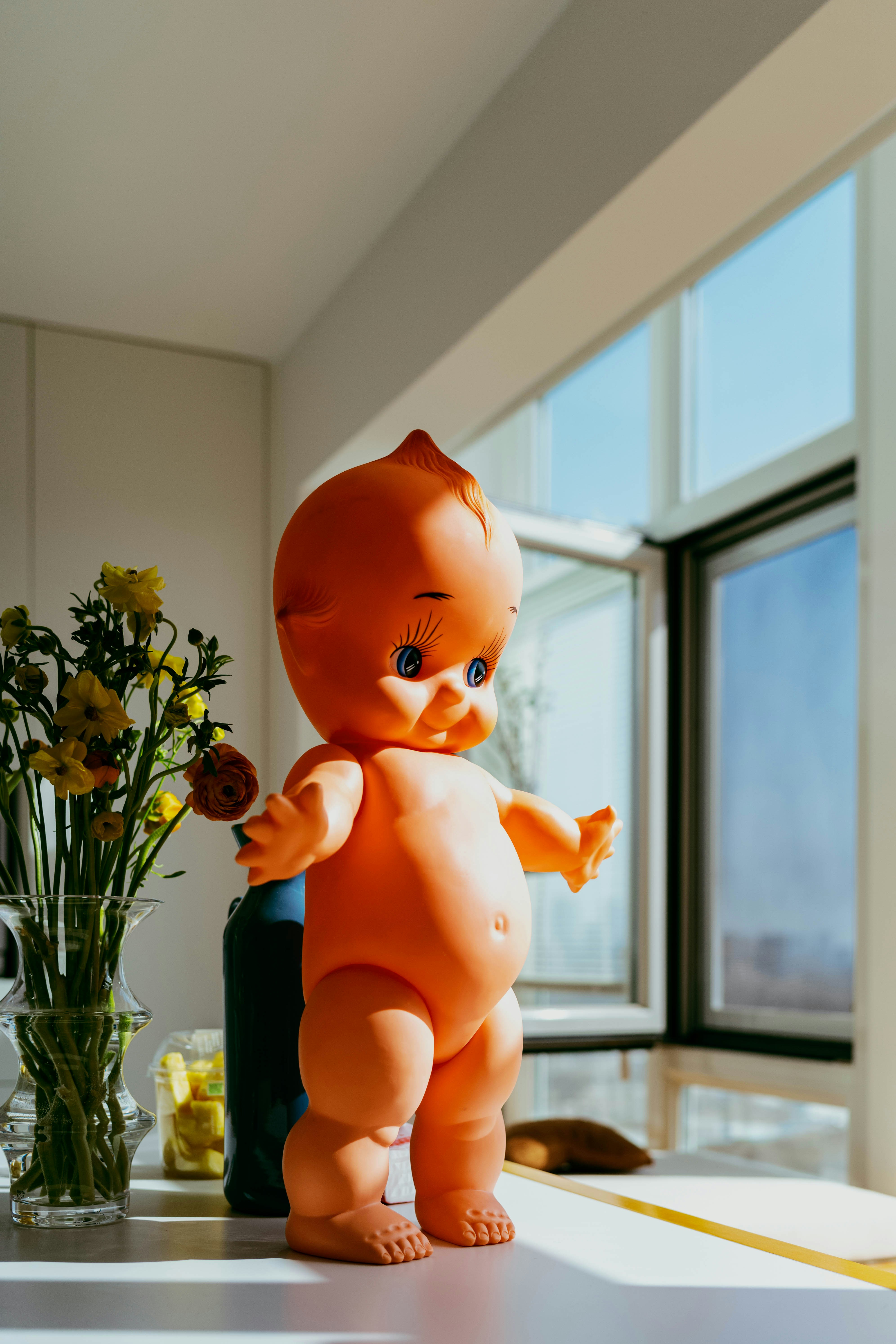 Sunlit Orange Doll Poised by Window Amid Fresh Flowers