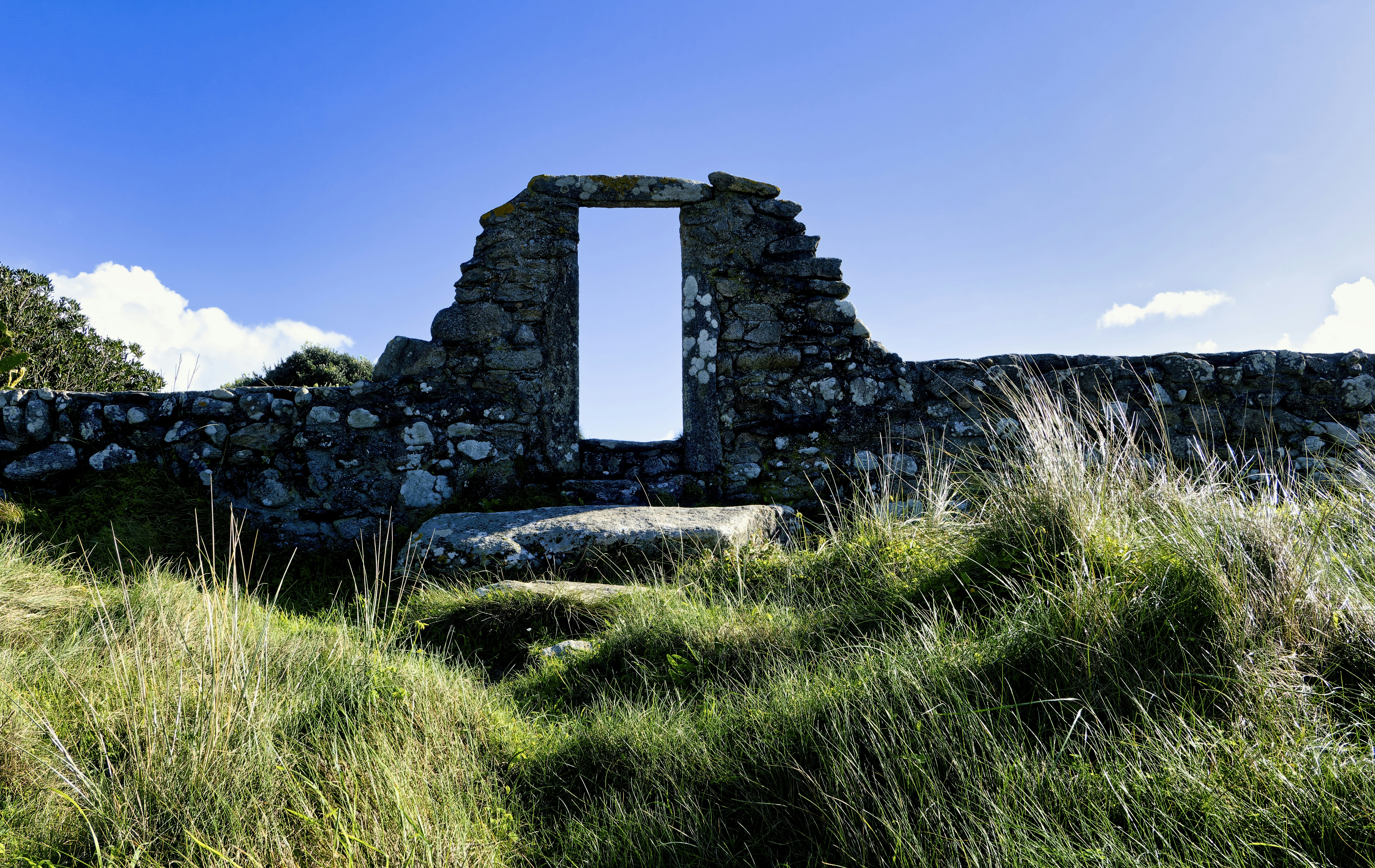 Ancient stone ruins with an open doorway framed by lush grass and a clear blue sky.