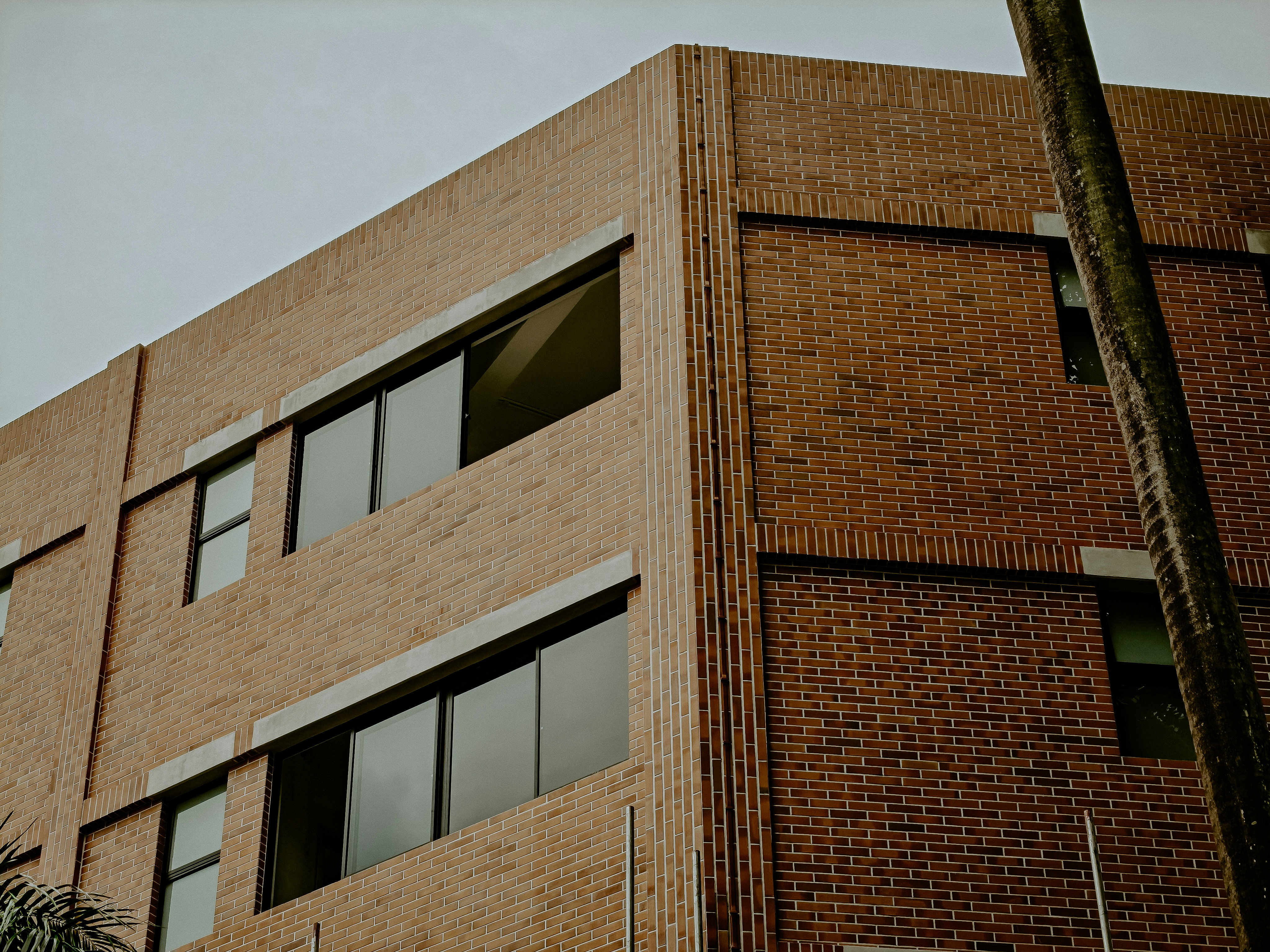 Corner view of a brick building with rectangular windows under a pale sky.