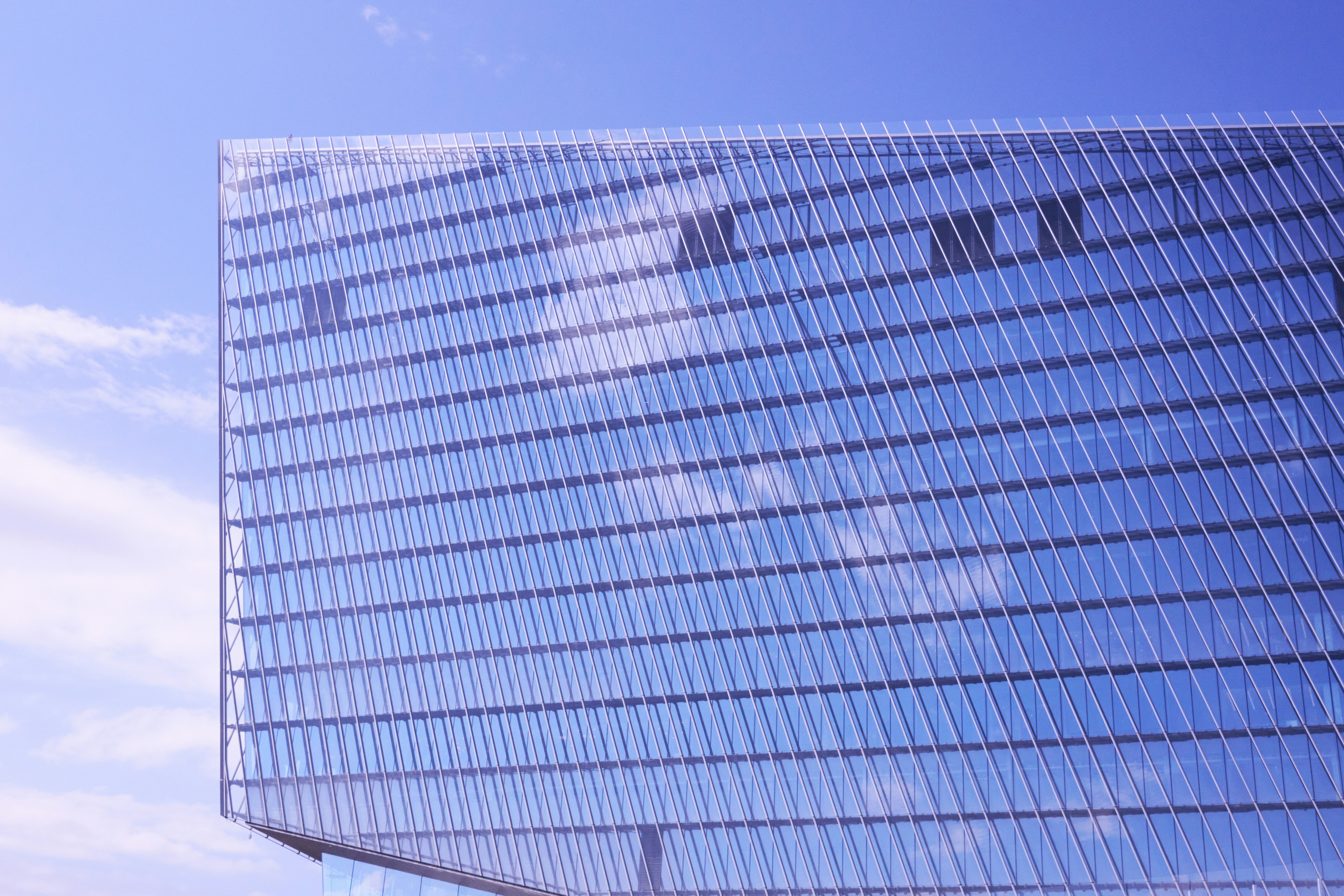 Modern glass building facade reflecting the blue sky and clouds.