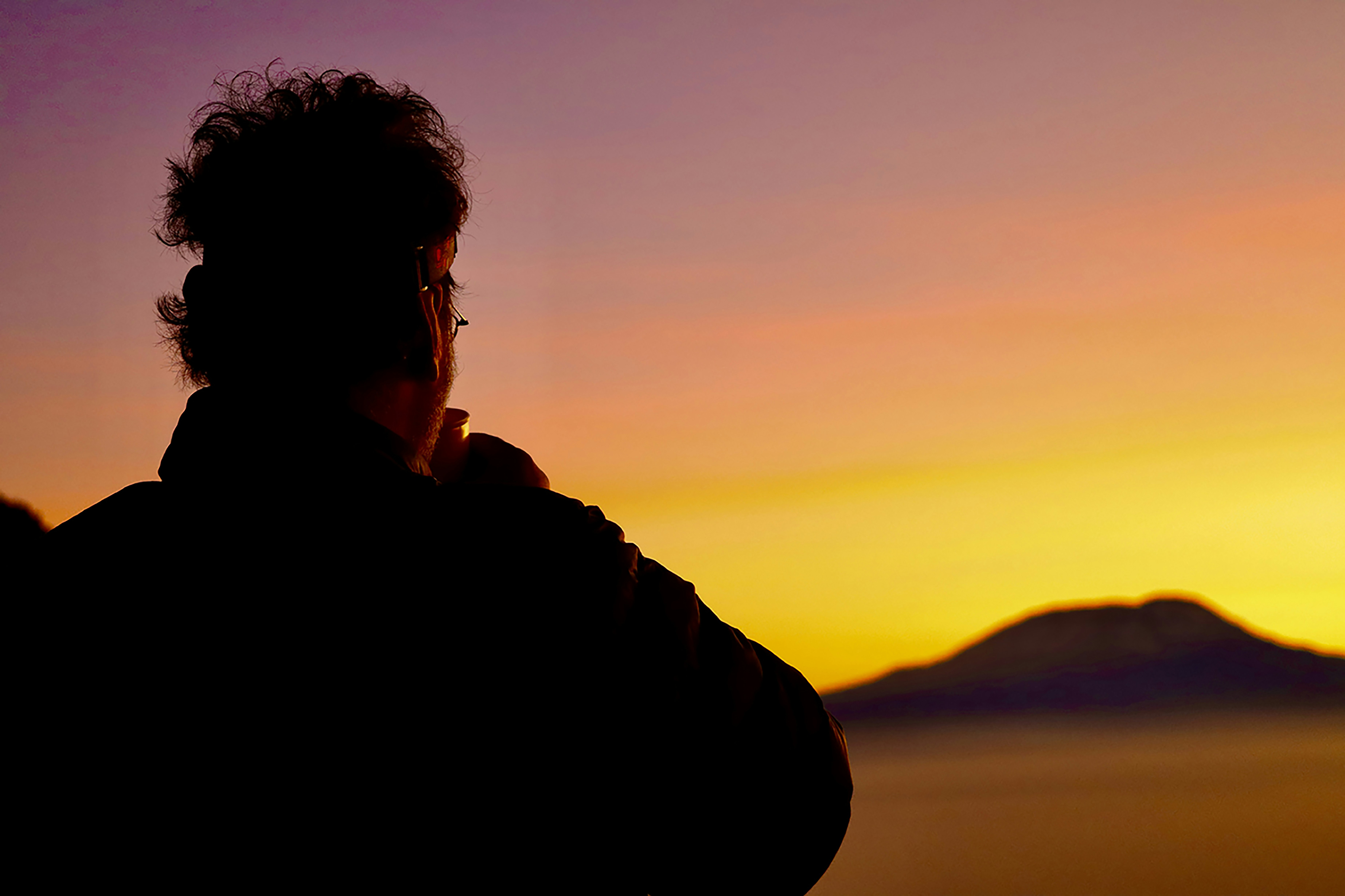 Silhouette of a person gazing at a vibrant sunrise over Mount Kilimanjaro.
