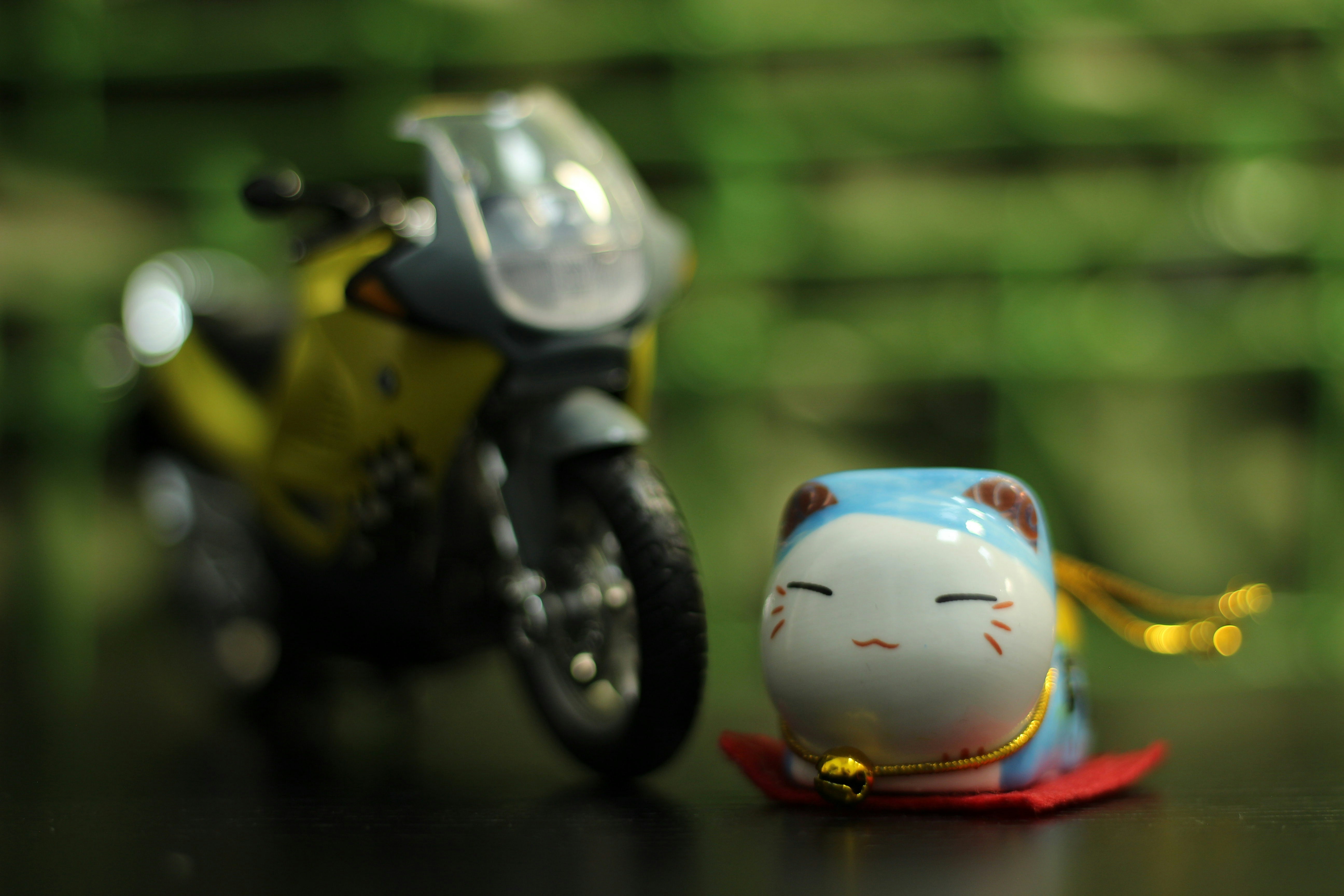 A Tiny Parade: Yellow Motorcycle Framing a Calm Cat Figurine