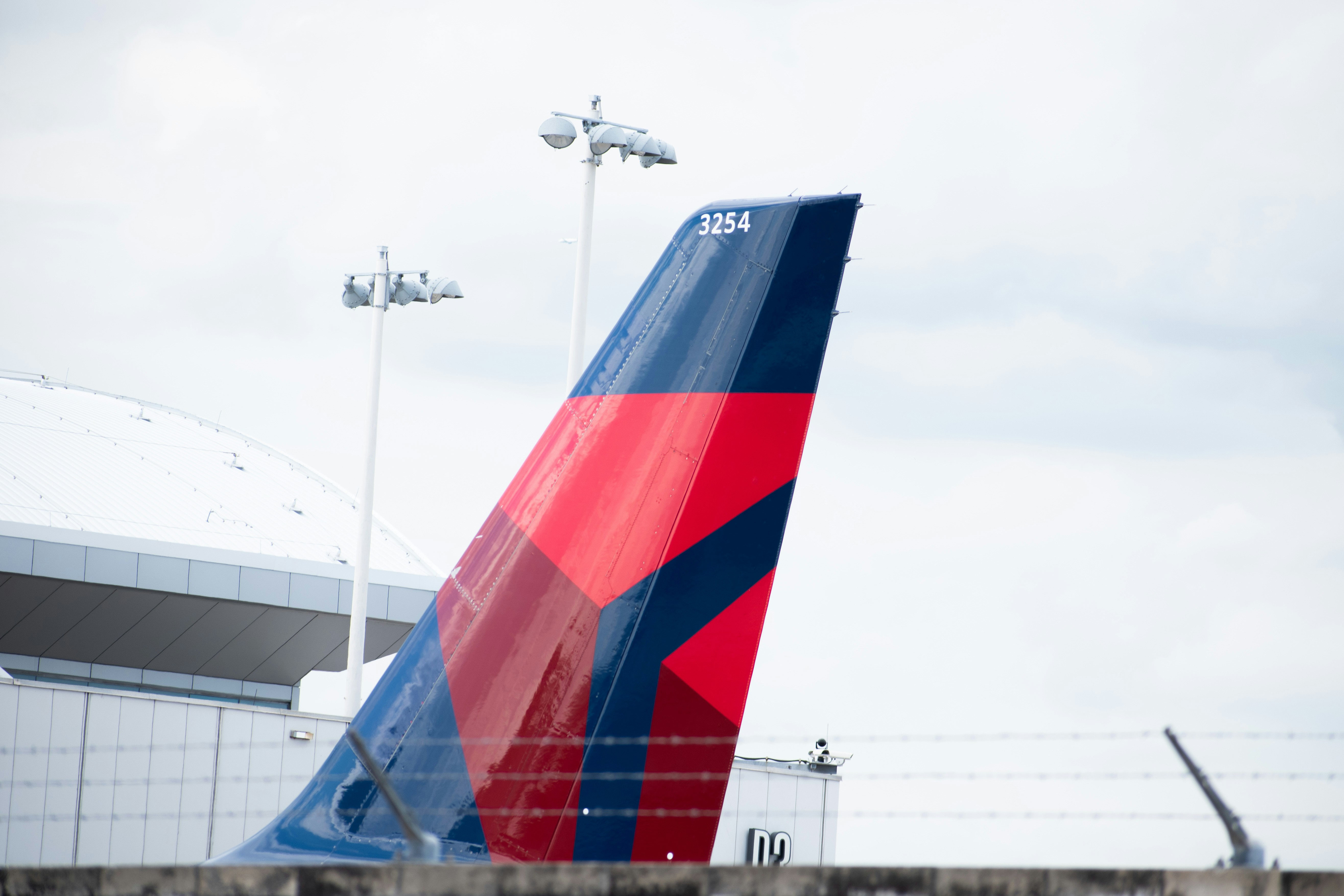 Airliner tailfin with a geometric design set against a cloudy sky at an airport.
