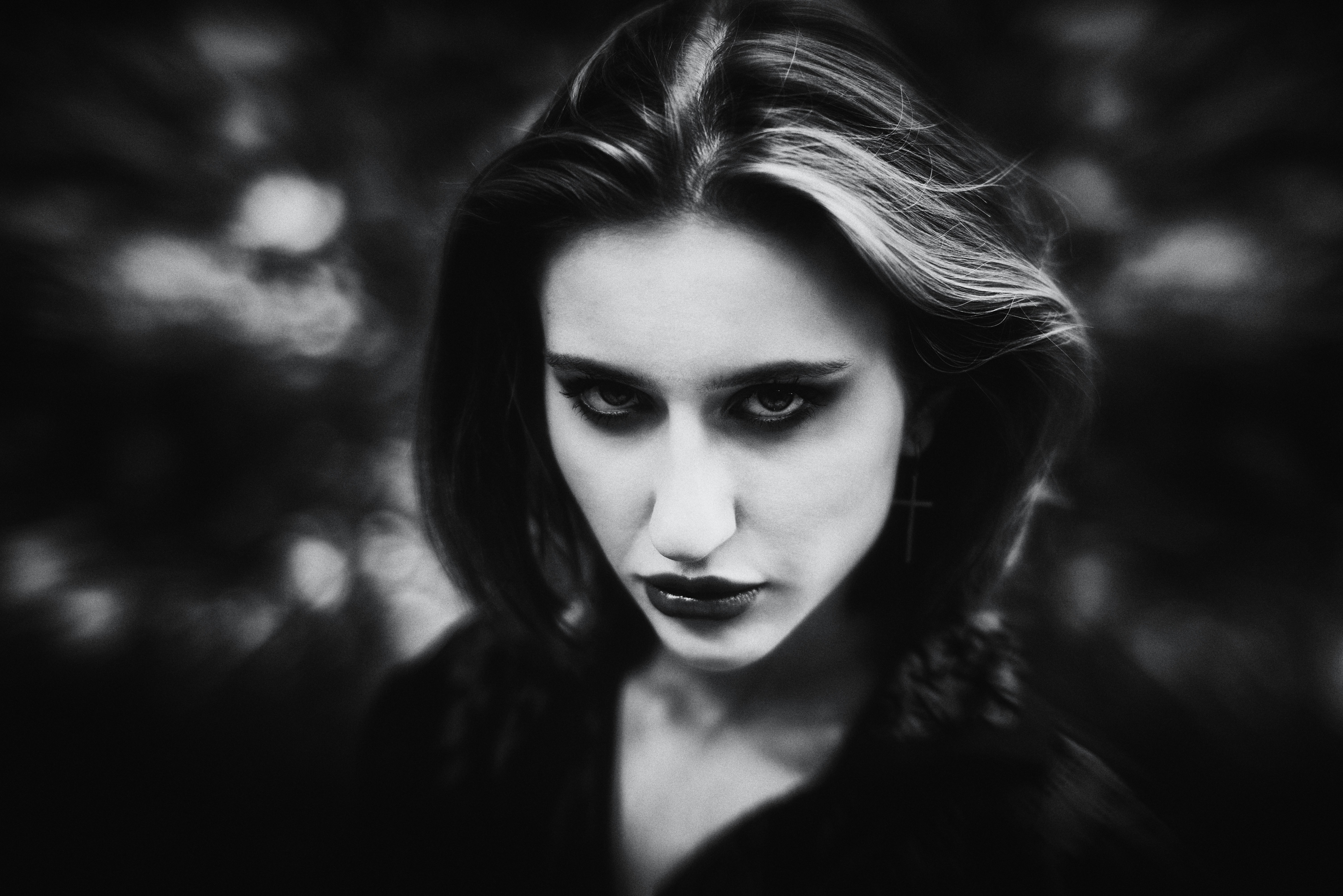 Monochrome portrait of a person with piercing eyes and a cross earring against a blurred background.