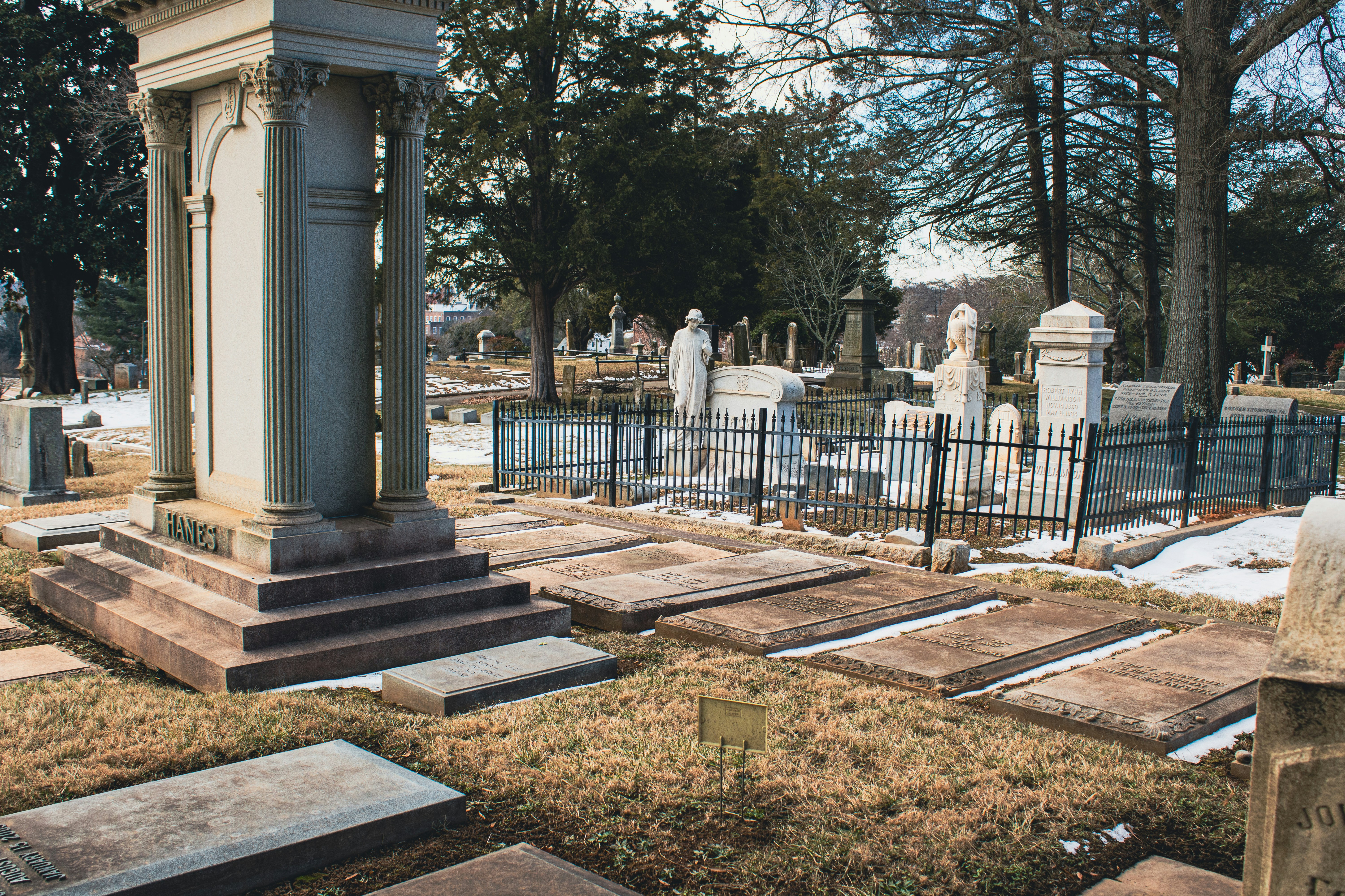 Historic cemetery with ornate tombstones and statues amid a winter landscape.