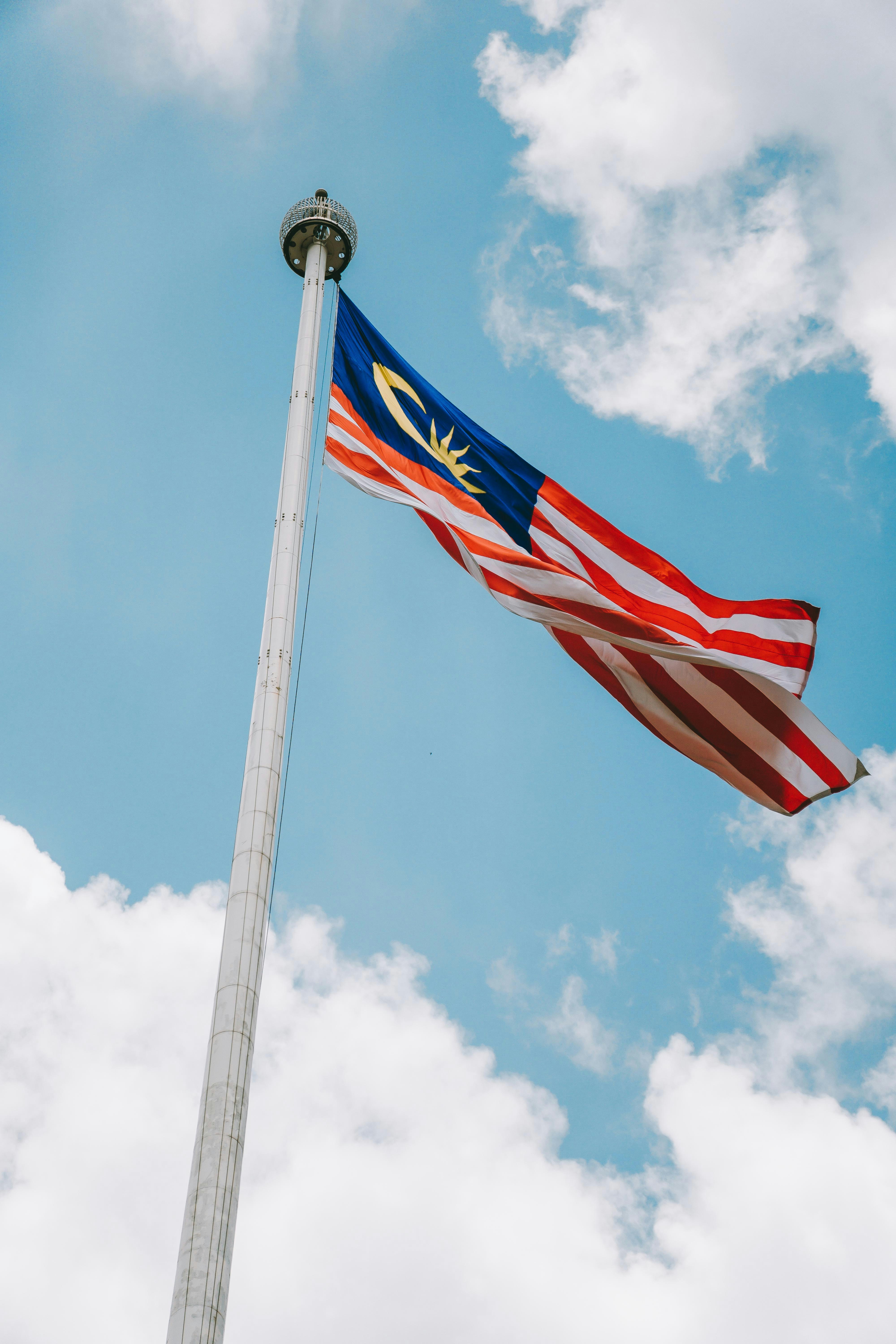 Malaysian flag billowing against a bright blue sky with fluffy clouds, showcasing national pride and identity.
