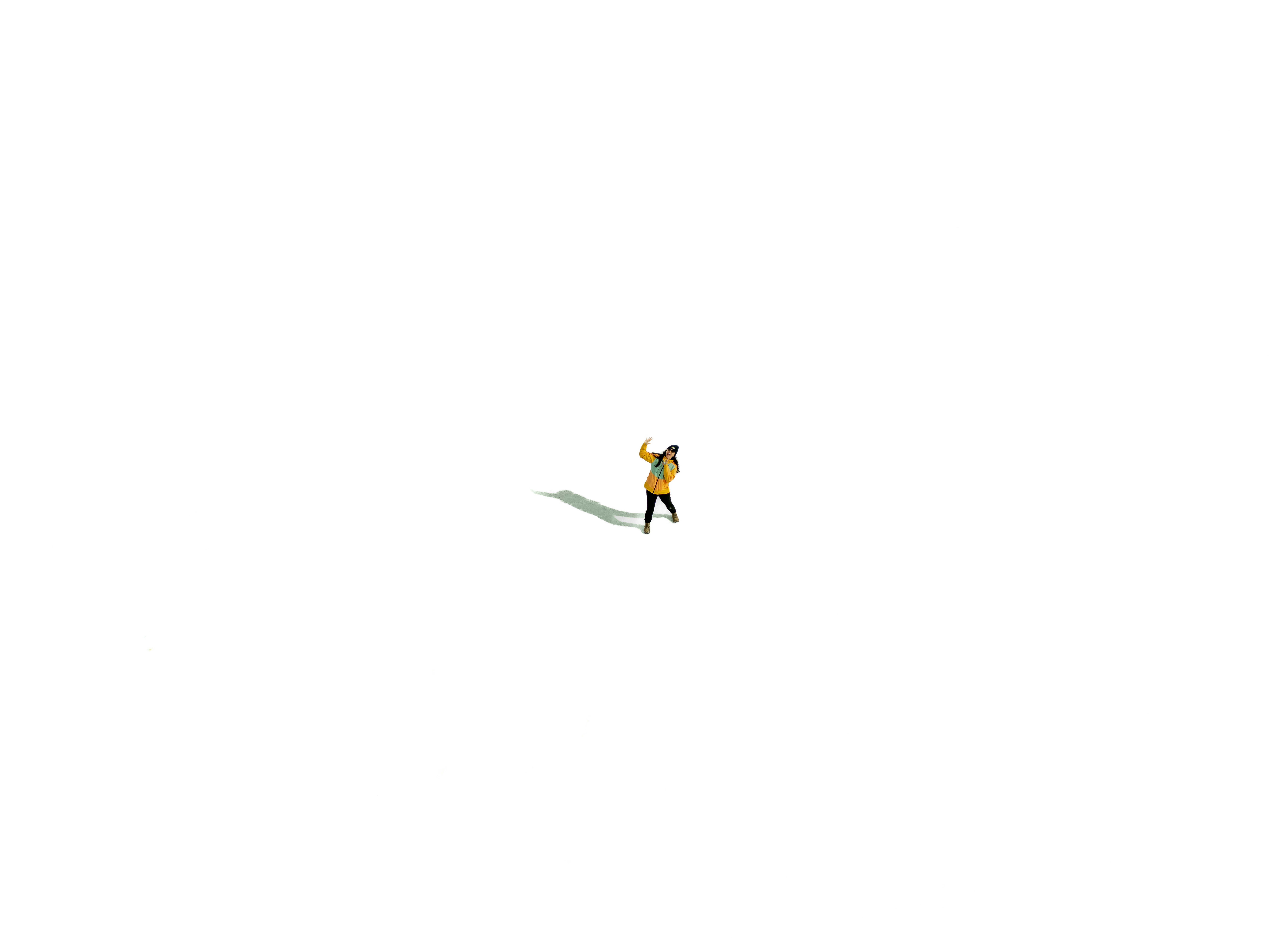 A lone figure in a yellow jacket traverses a vast, empty expanse, casting a long shadow. The simplicity emphasizes the journey ahead.