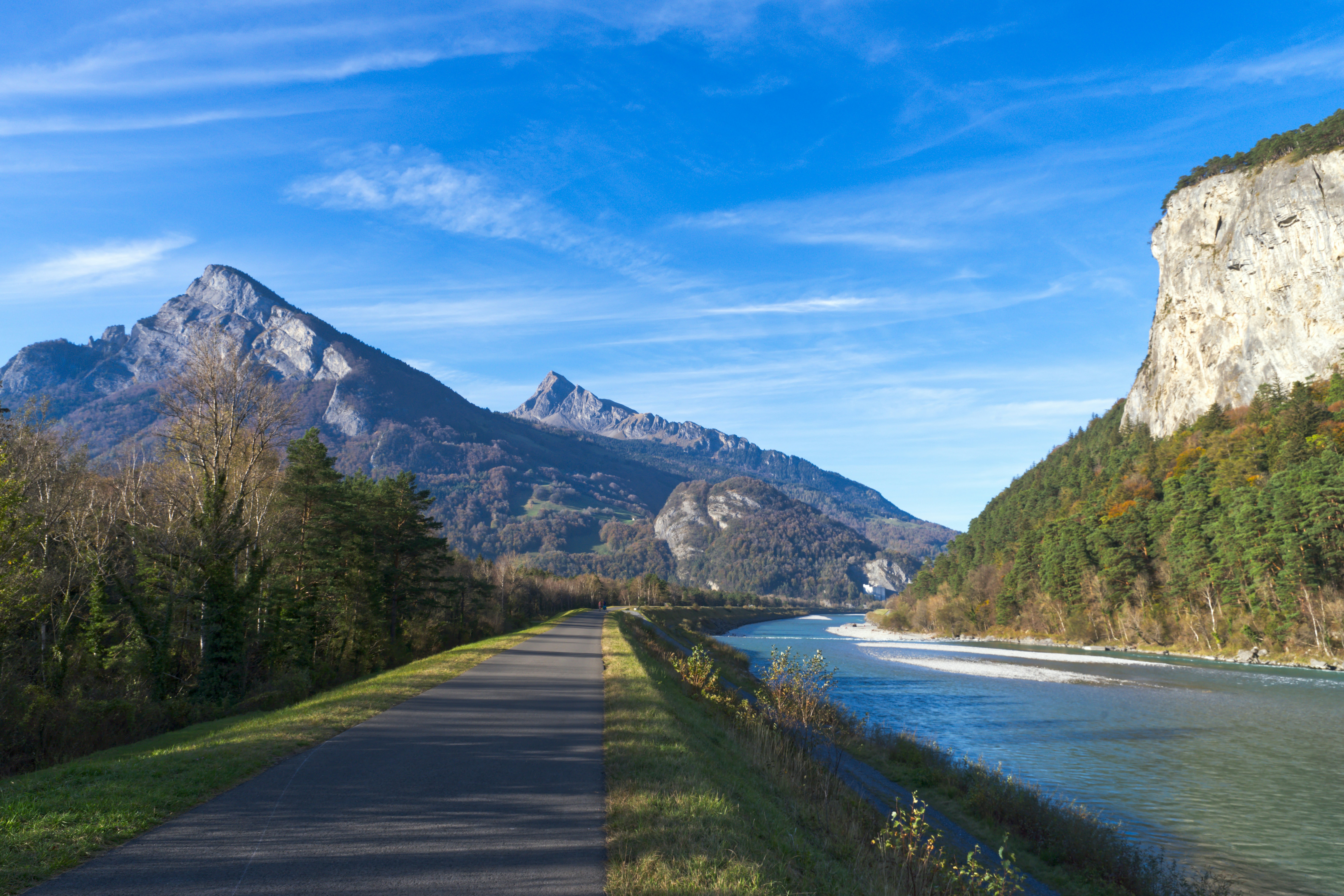 Mountainous landscape with a winding river and a path under a clear blue sky.
